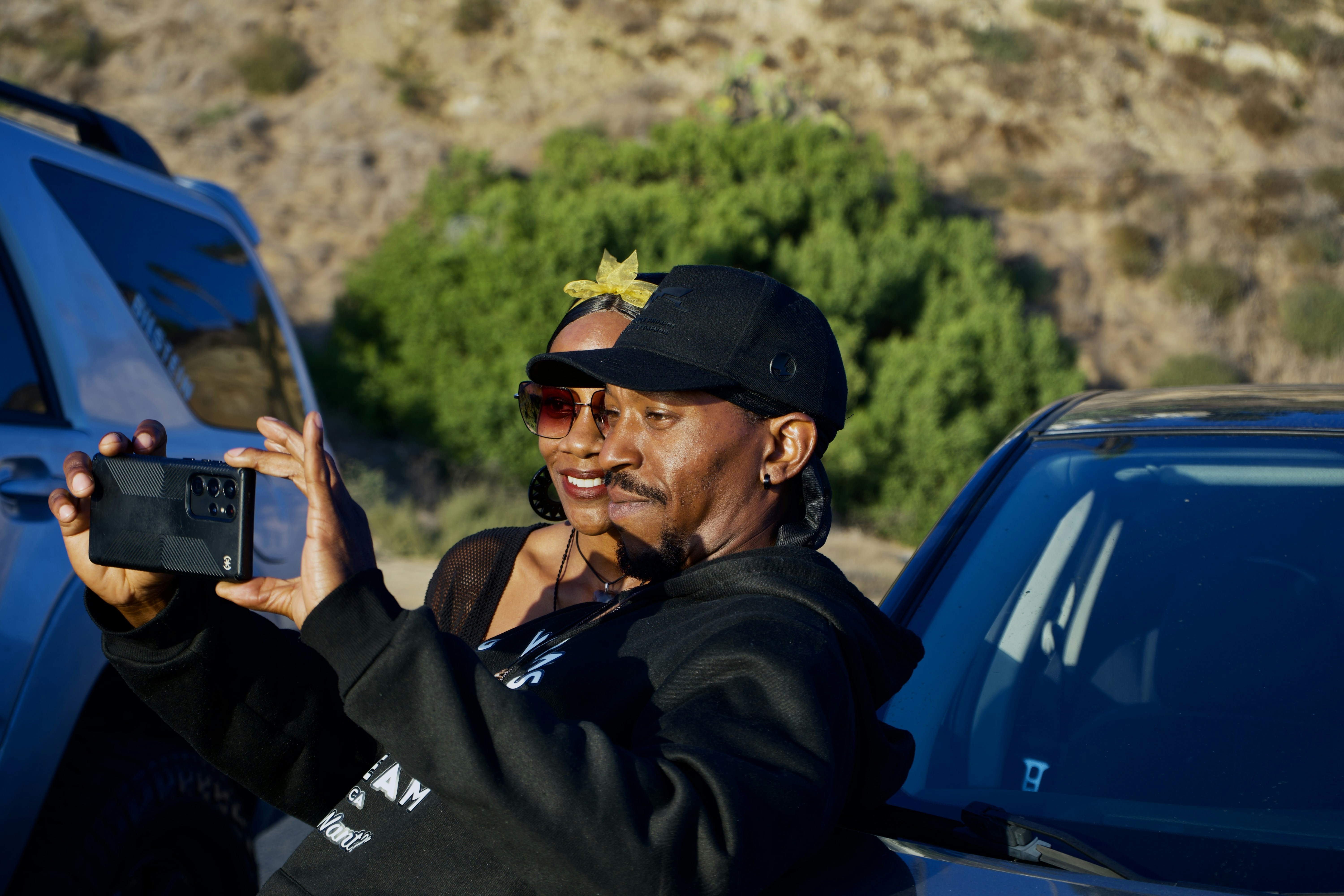Driveway Duo: A Sunlit Selfie Between Blue SUVs