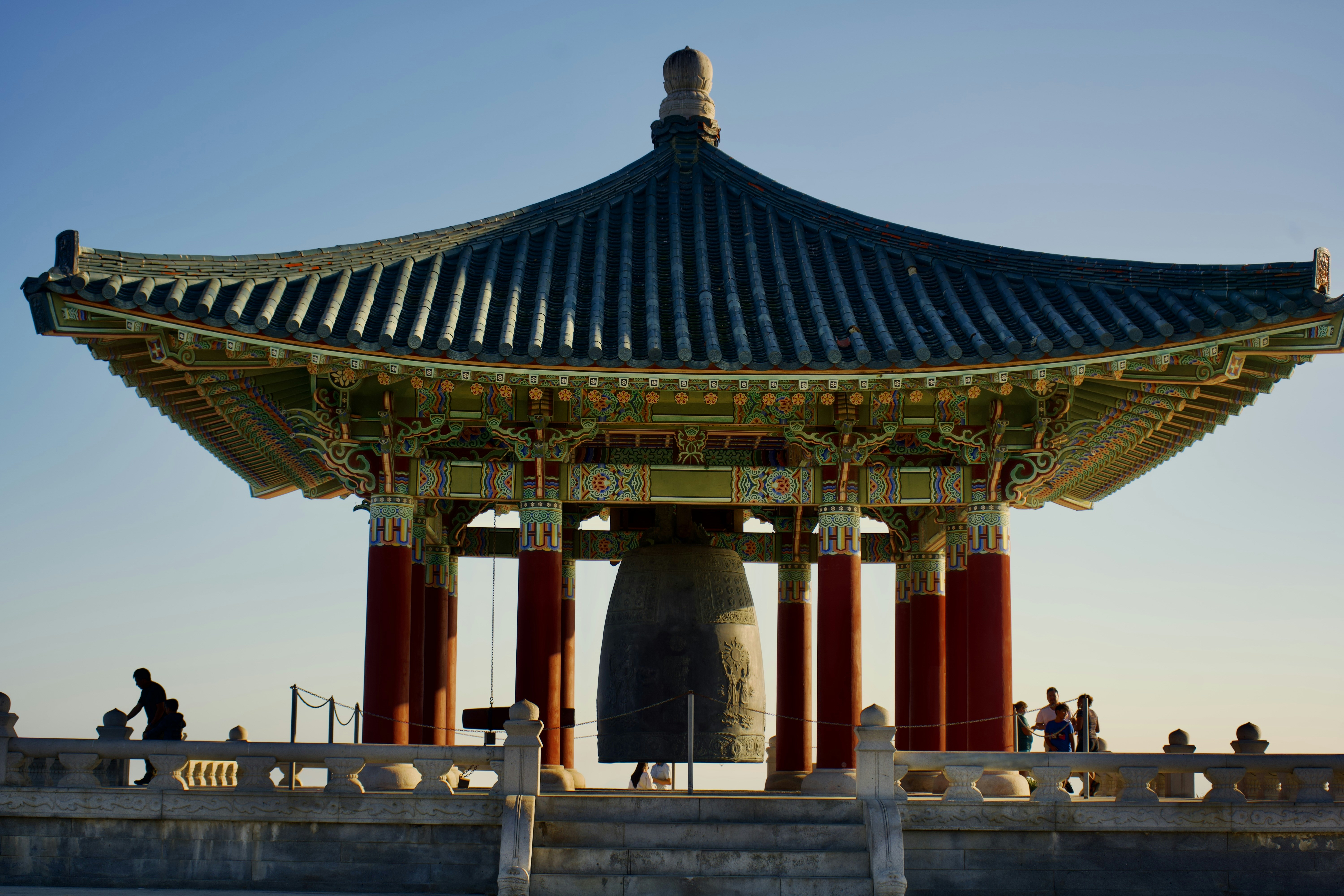 Ornate pagoda with a large bell beneath, framed by intricate wooden columns and vivid colors.