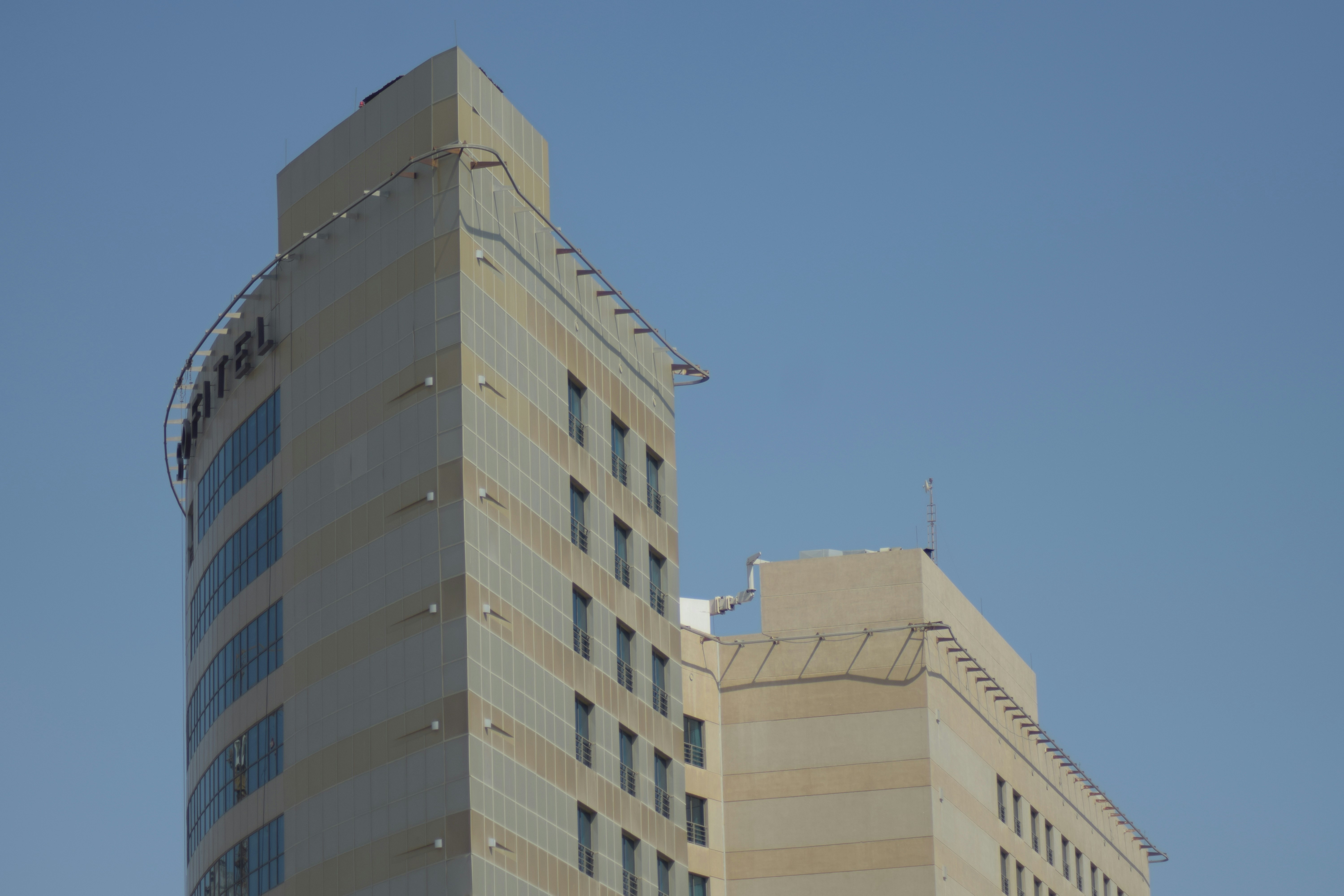 A modern high-rise building featuring sleek glass and concrete design, with a clear blue sky serving as a backdrop.