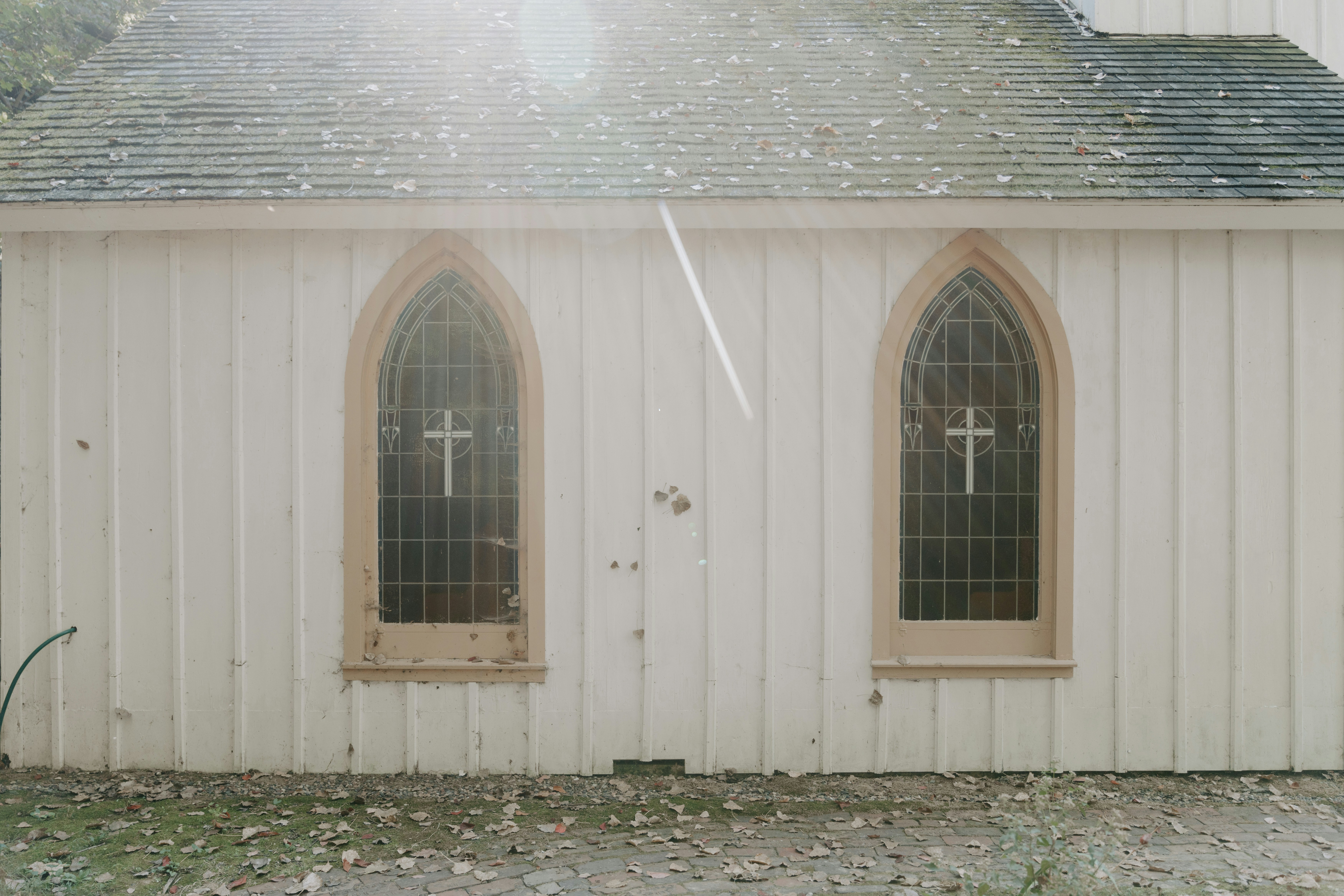 Sunlight streaming onto the side of a rustic chapel with two arched windows featuring crosses.