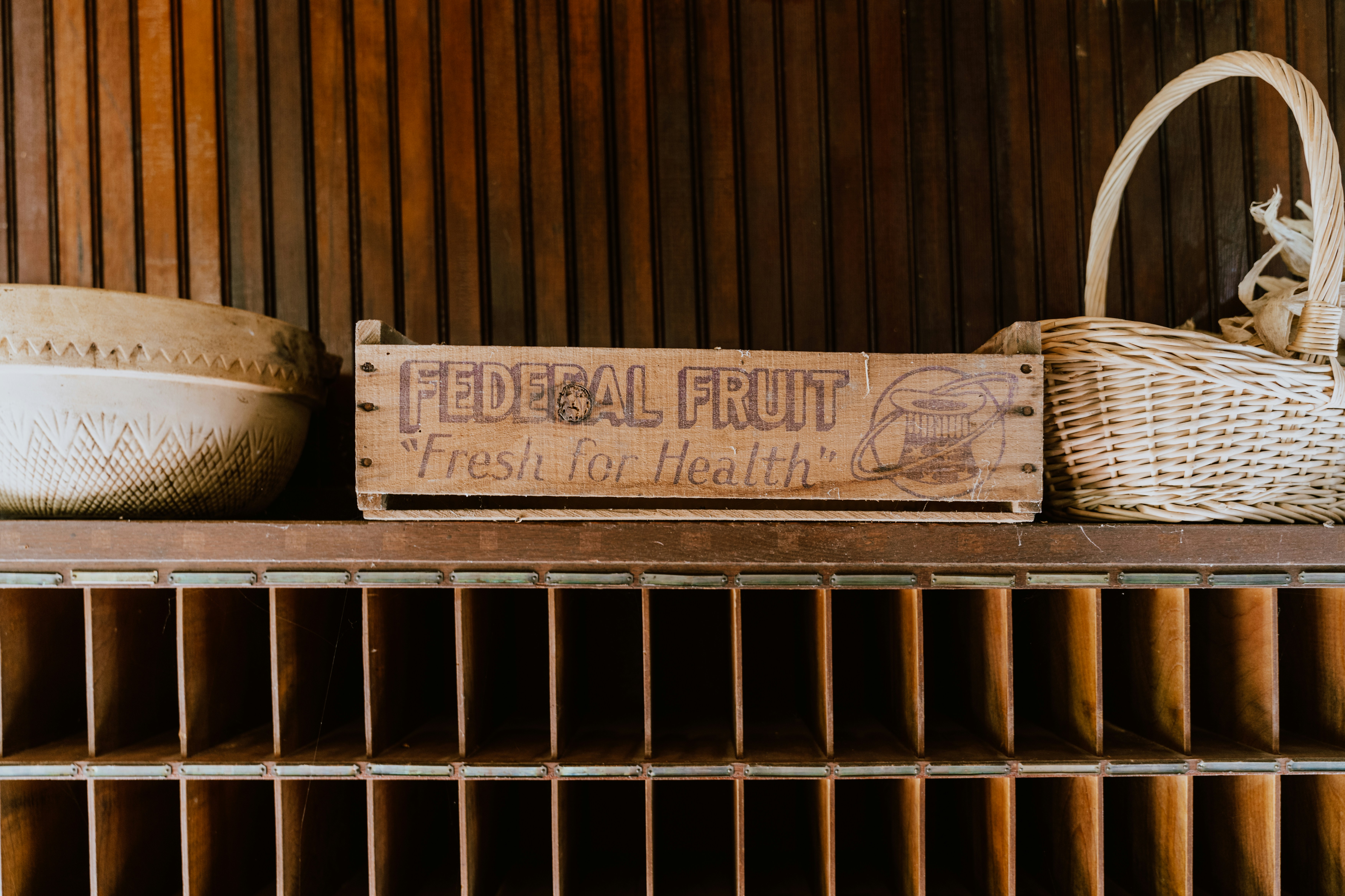 Vintage wooden crate and wicker baskets on a wooden shelf with vertical slats.