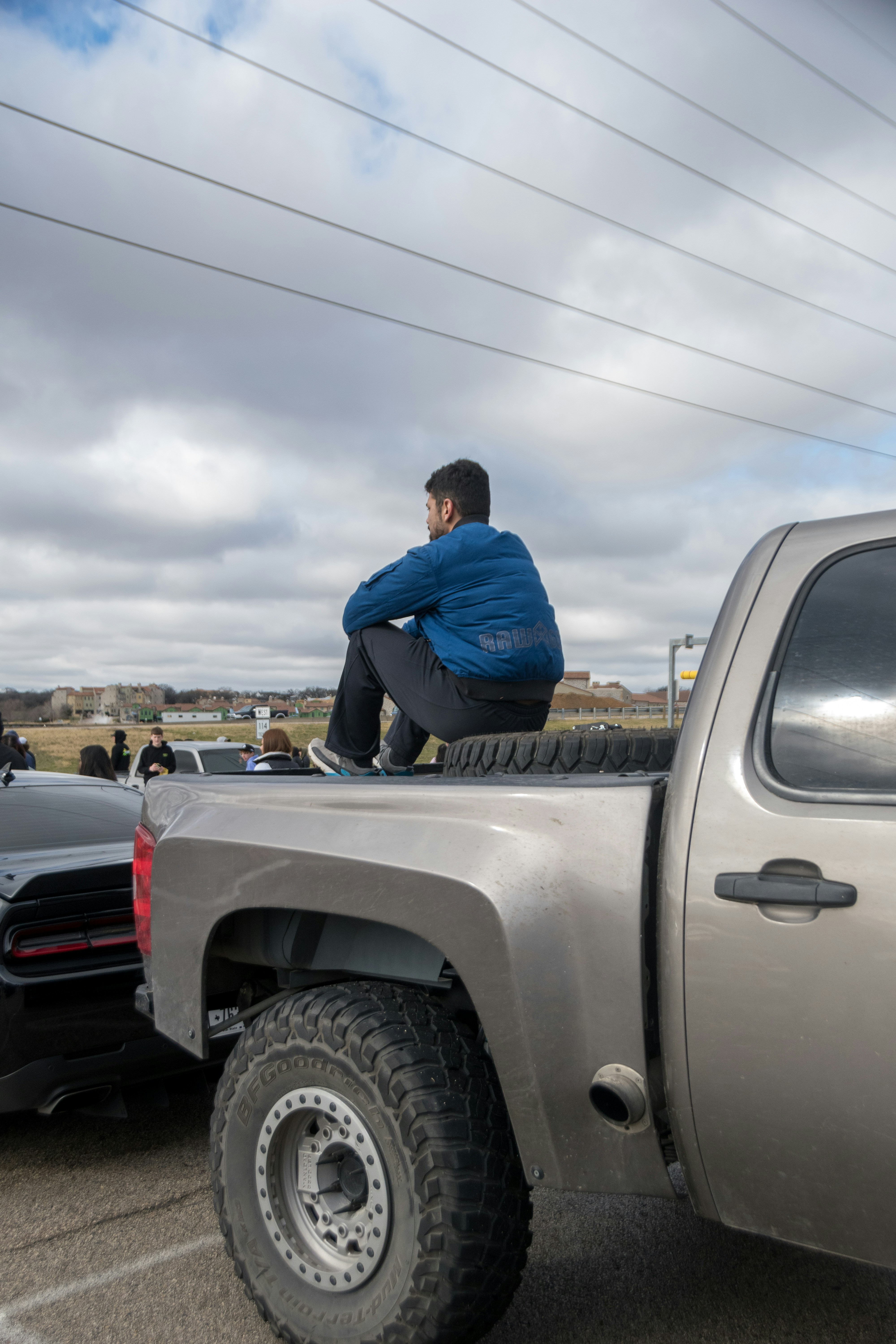 Man in blue jacket sits atop a silver pickup at a crowded overlook
