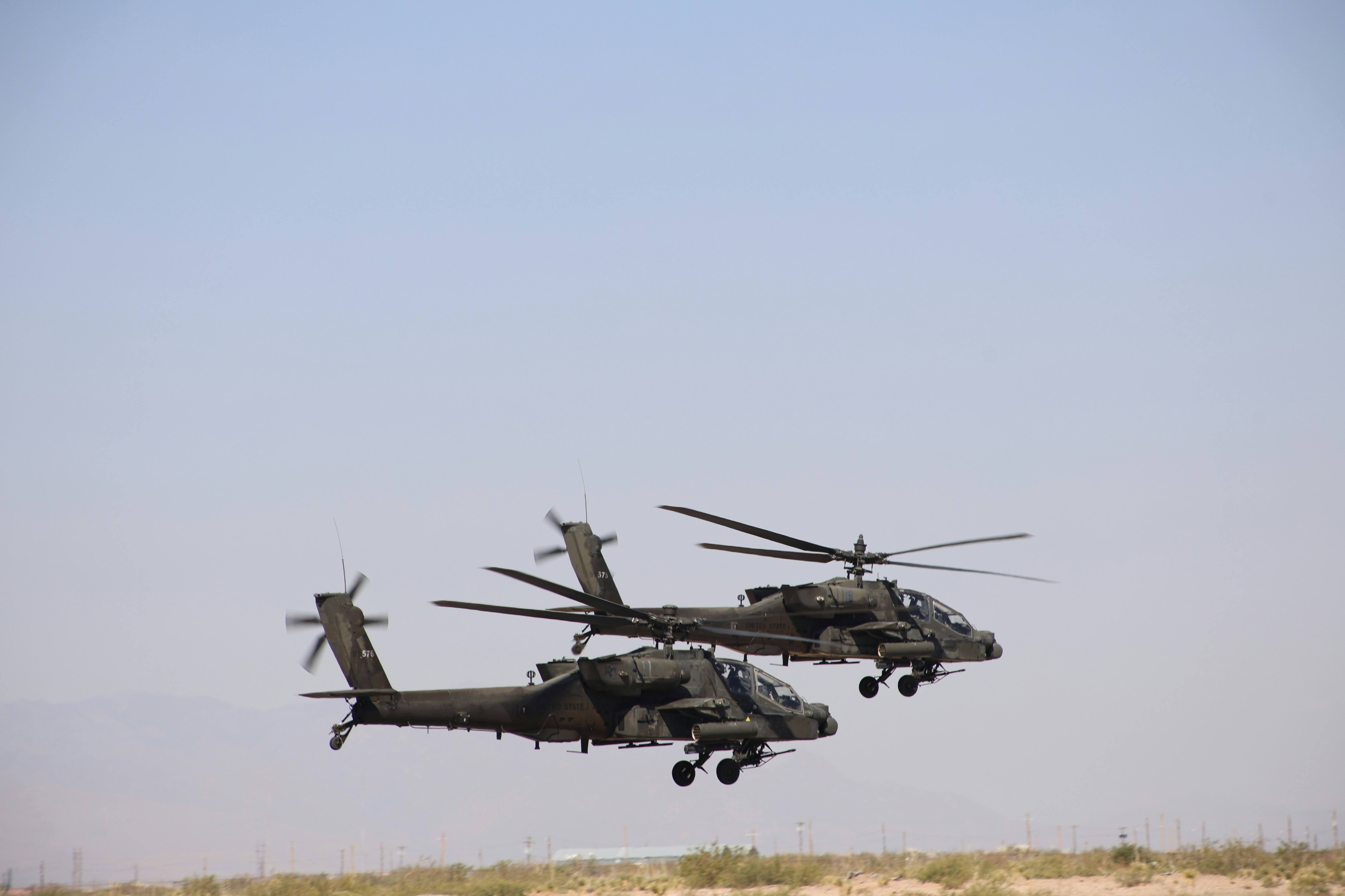 A couple of military helicopters flying over a field photo – Free El ...