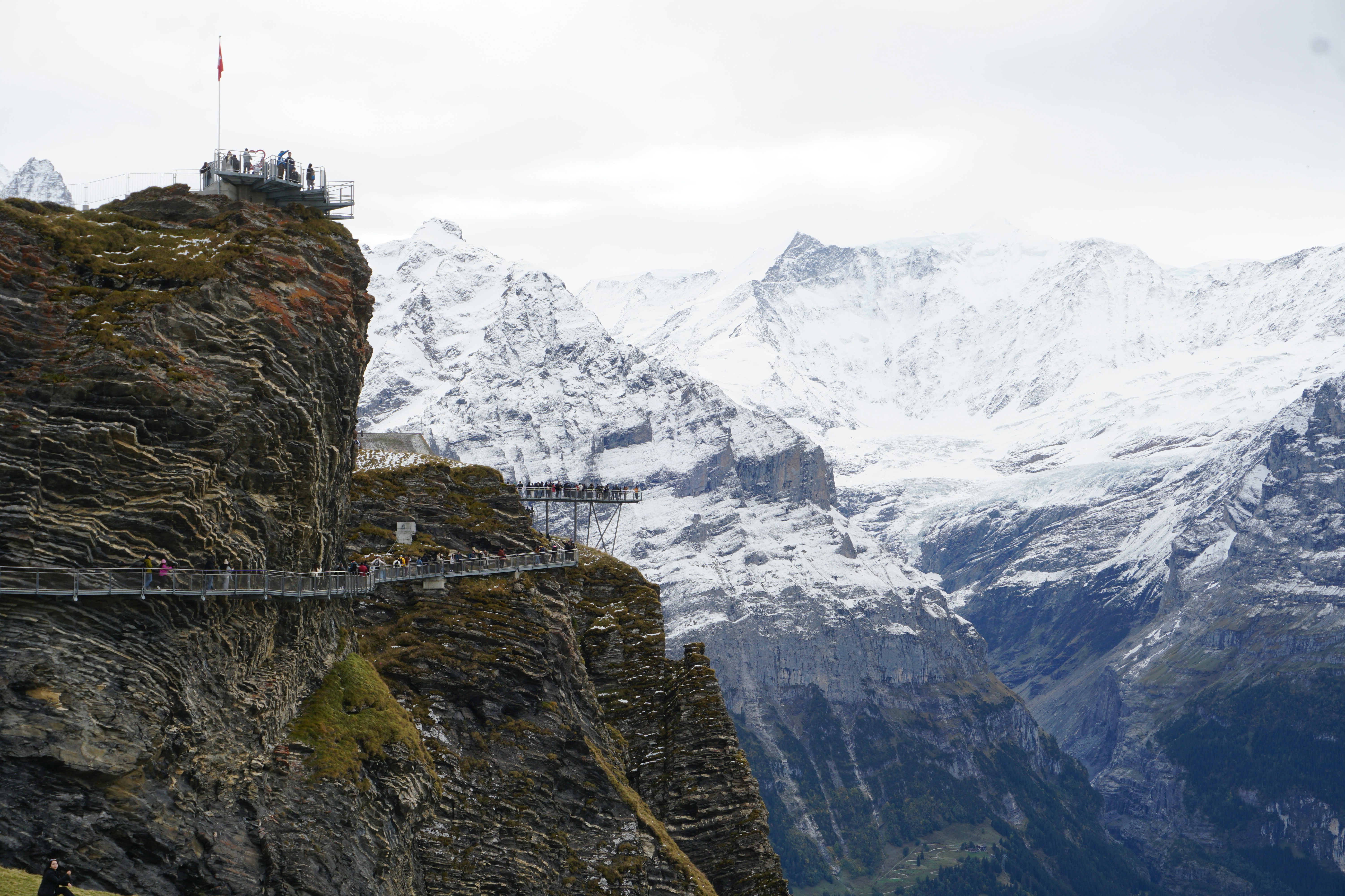 Flag at the Edge: Cliffside Walk Above Snow-Washed Peaks