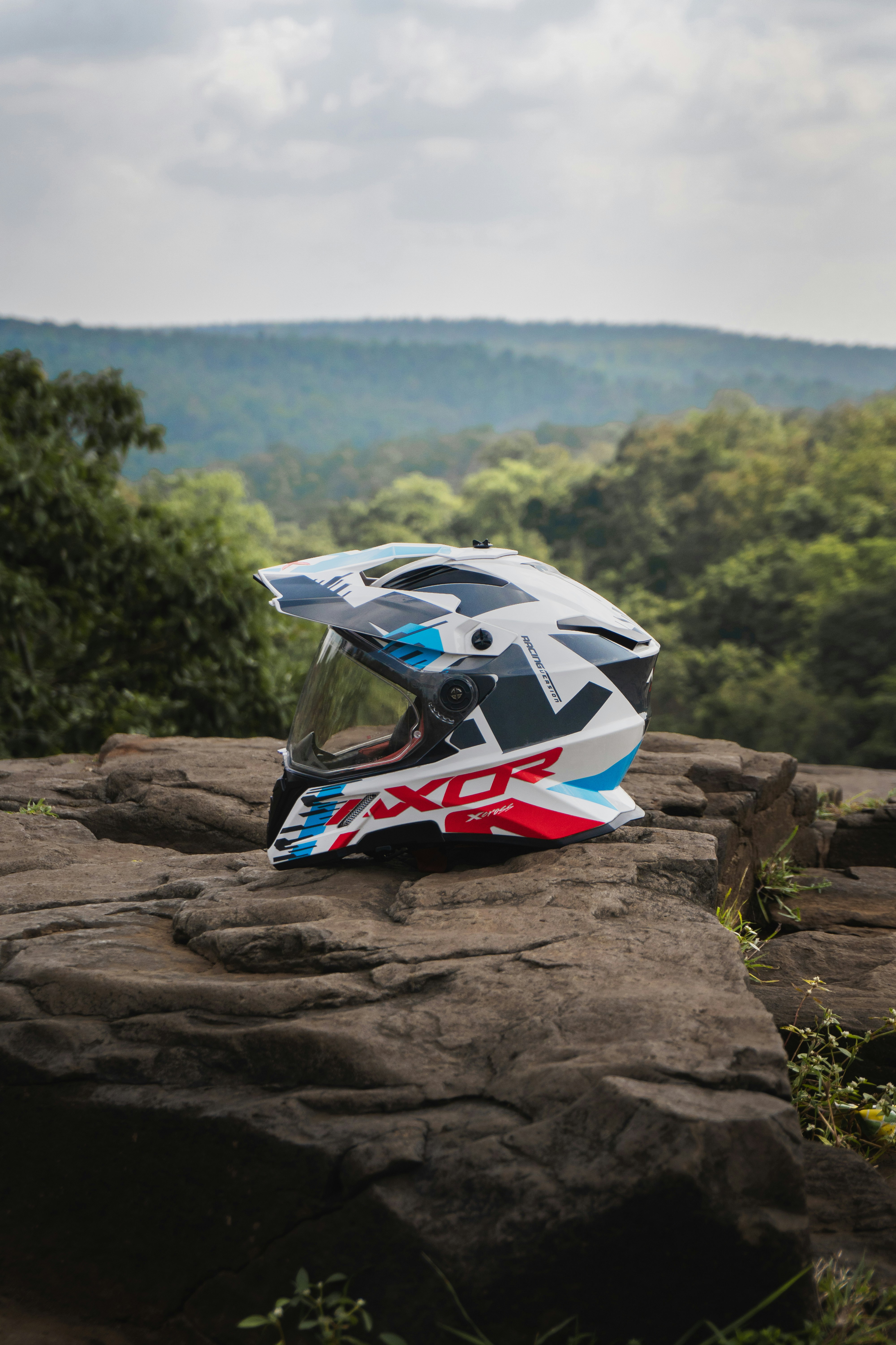 Rock-Ledge Sentinel: a motocross helmet resting on weathered stone with a rolling green valley behind