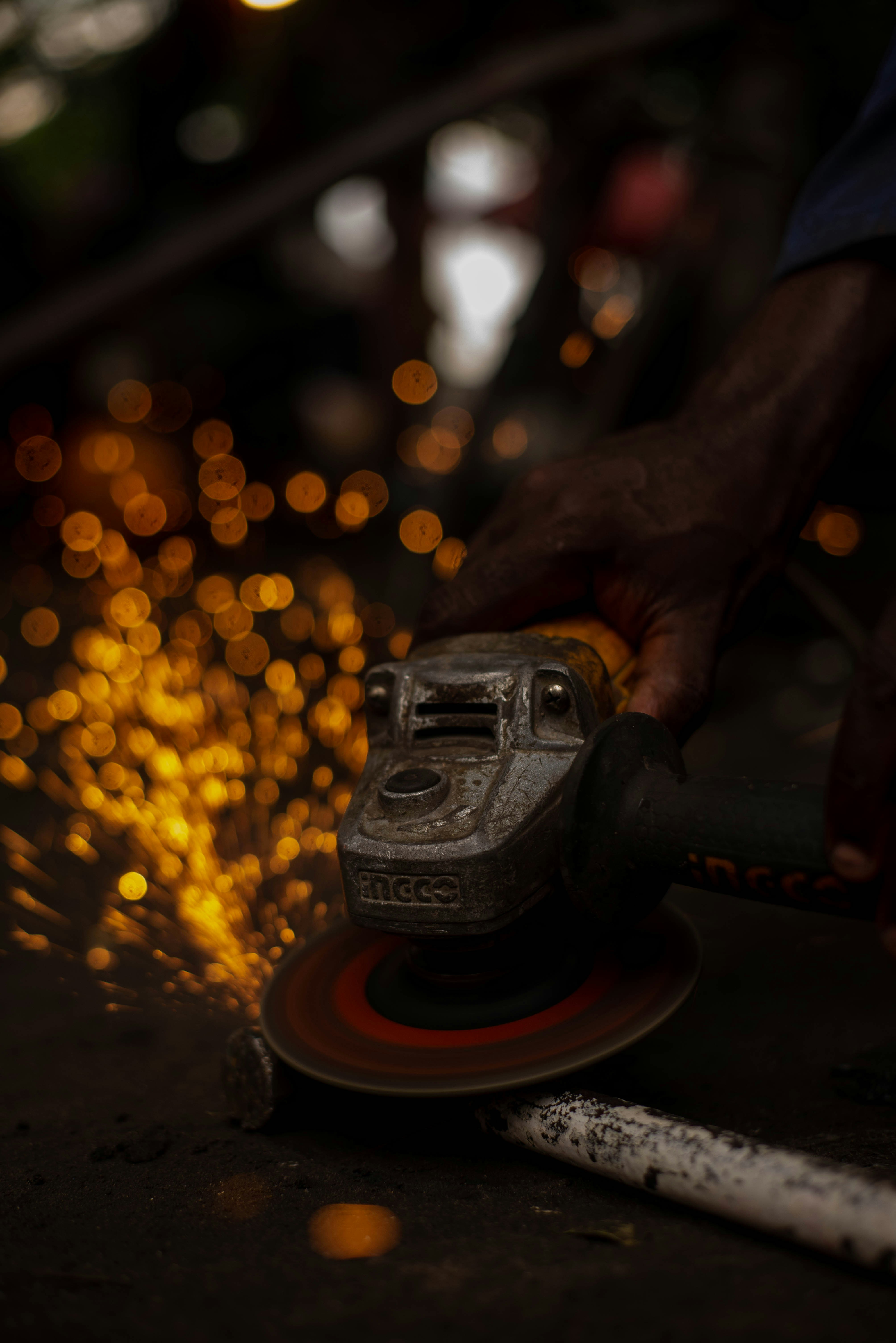 A craftsman skillfully operates a grinder, sending sparks flying against a blurred backdrop of warm bokeh lights. The scene captures the essence of manual labor and creativity.