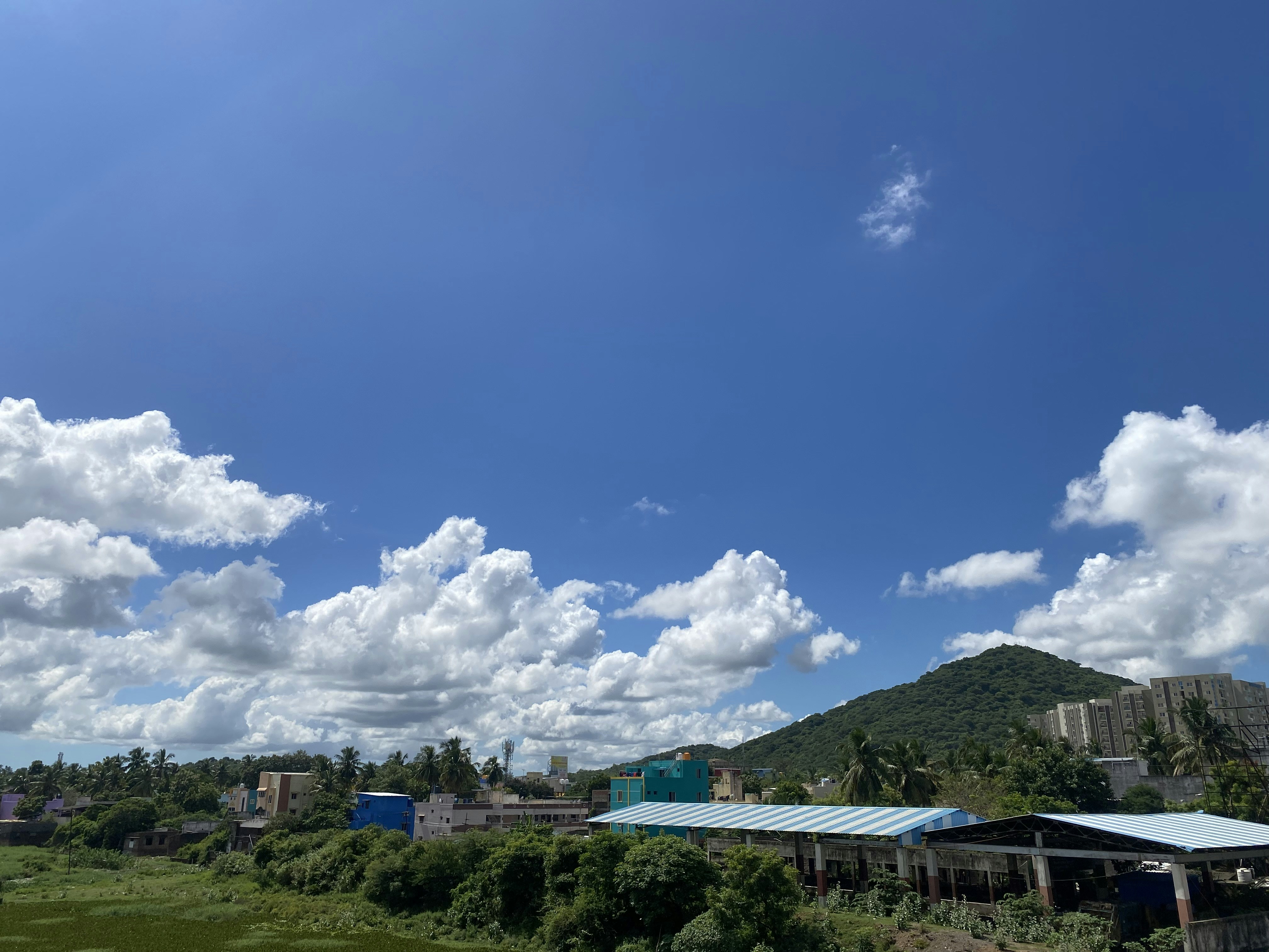 Lush green landscape with rolling hills beneath a vibrant blue sky dotted with fluffy clouds.