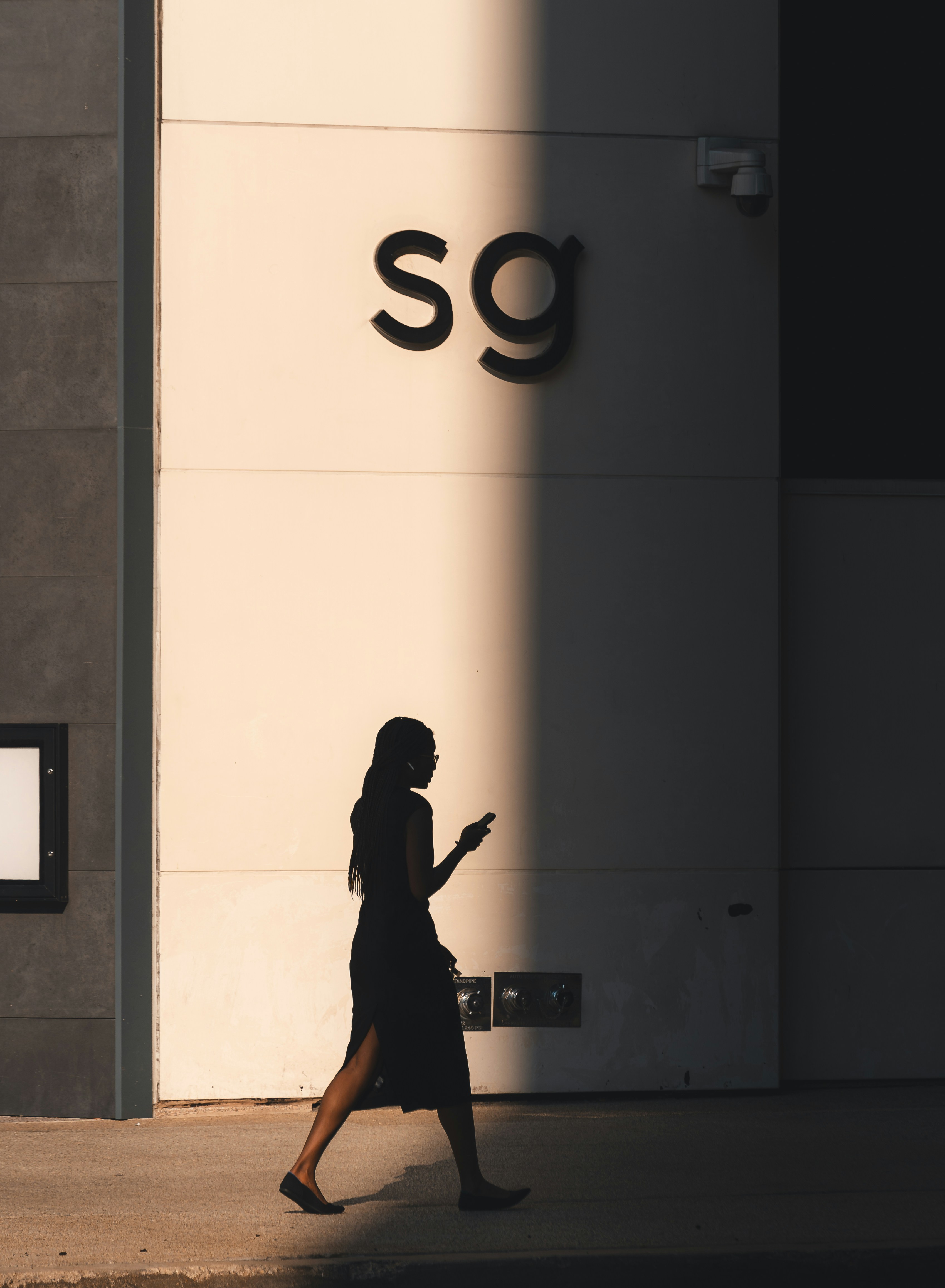 A woman walking down a sidewalk next to a tall building photo – Free ...