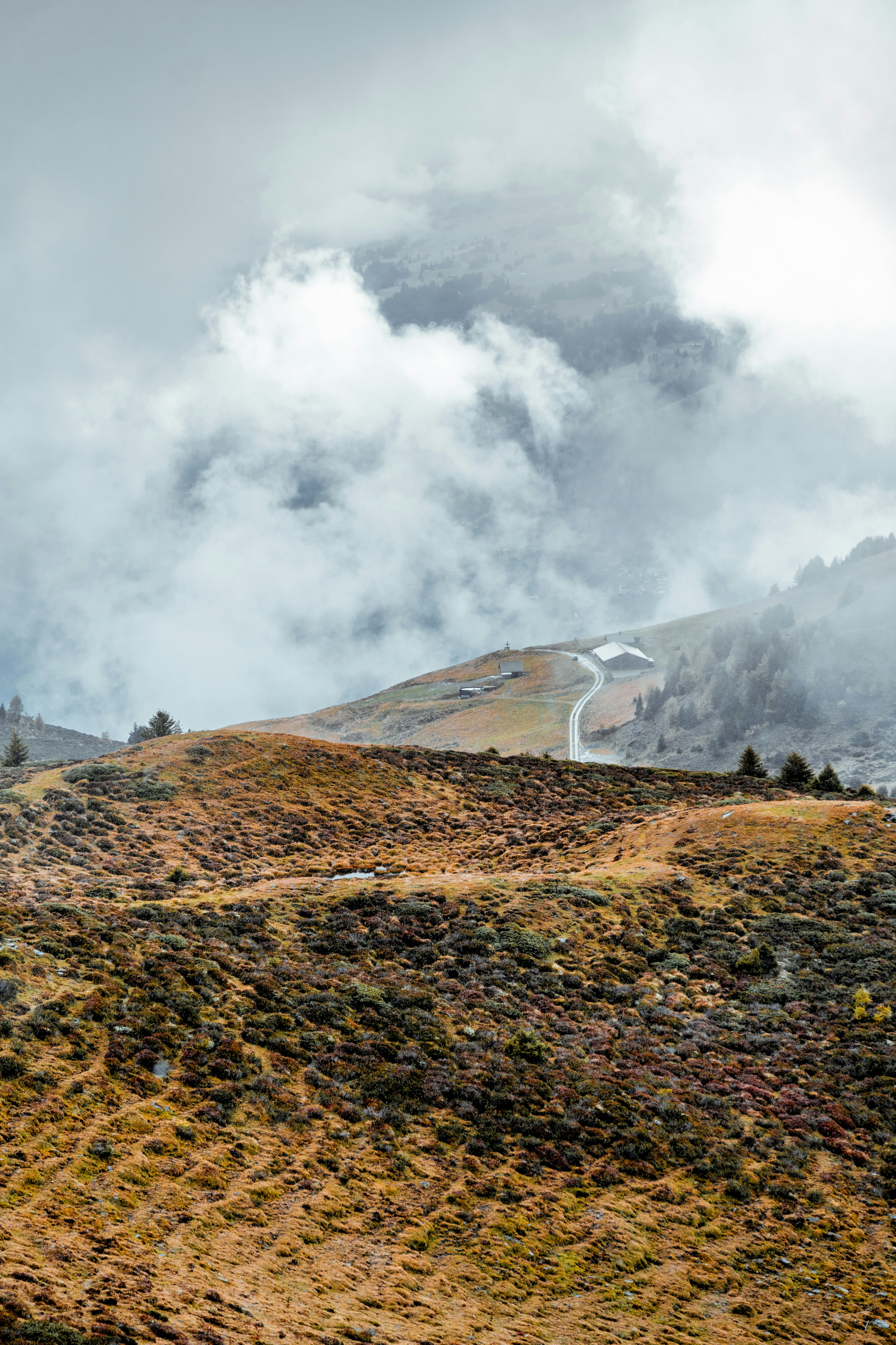 Winding road through mist-draped hills under a cloudy sky.