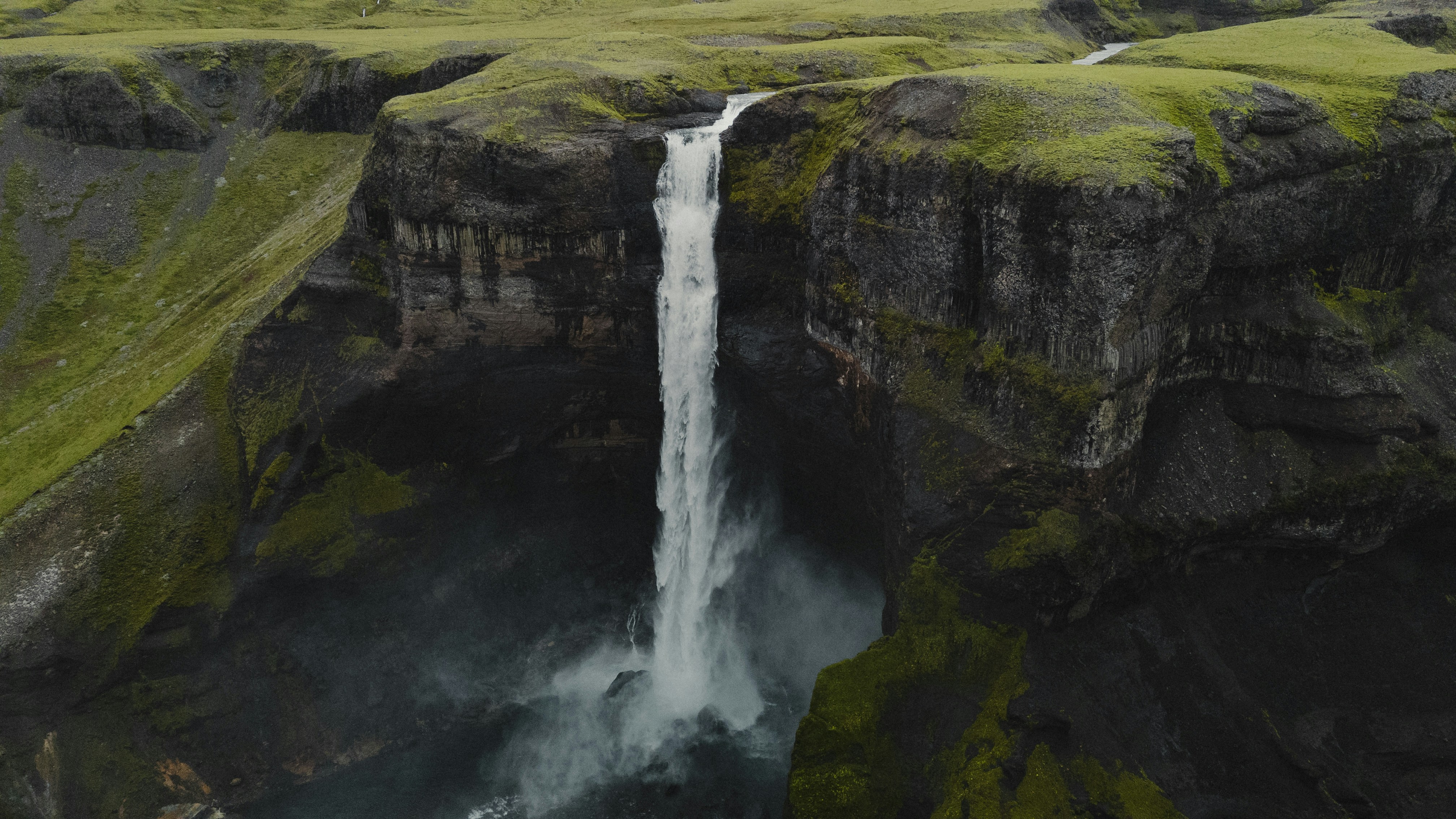 Tall waterfall plunging into a rugged canyon surrounded by lush green cliffs.