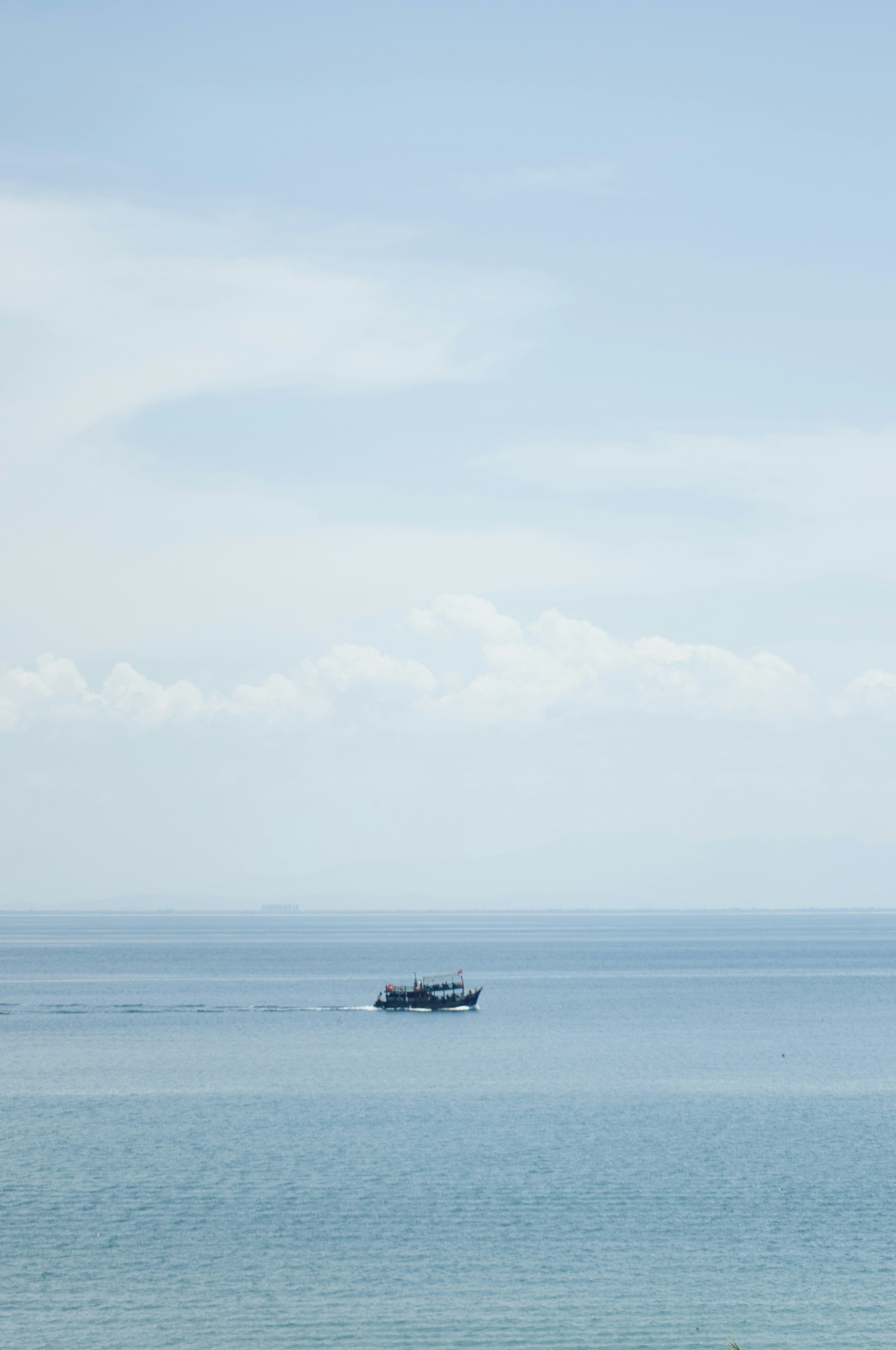 Low-Horizon Vessel: a tiny boat traverses a quiet blue expanse