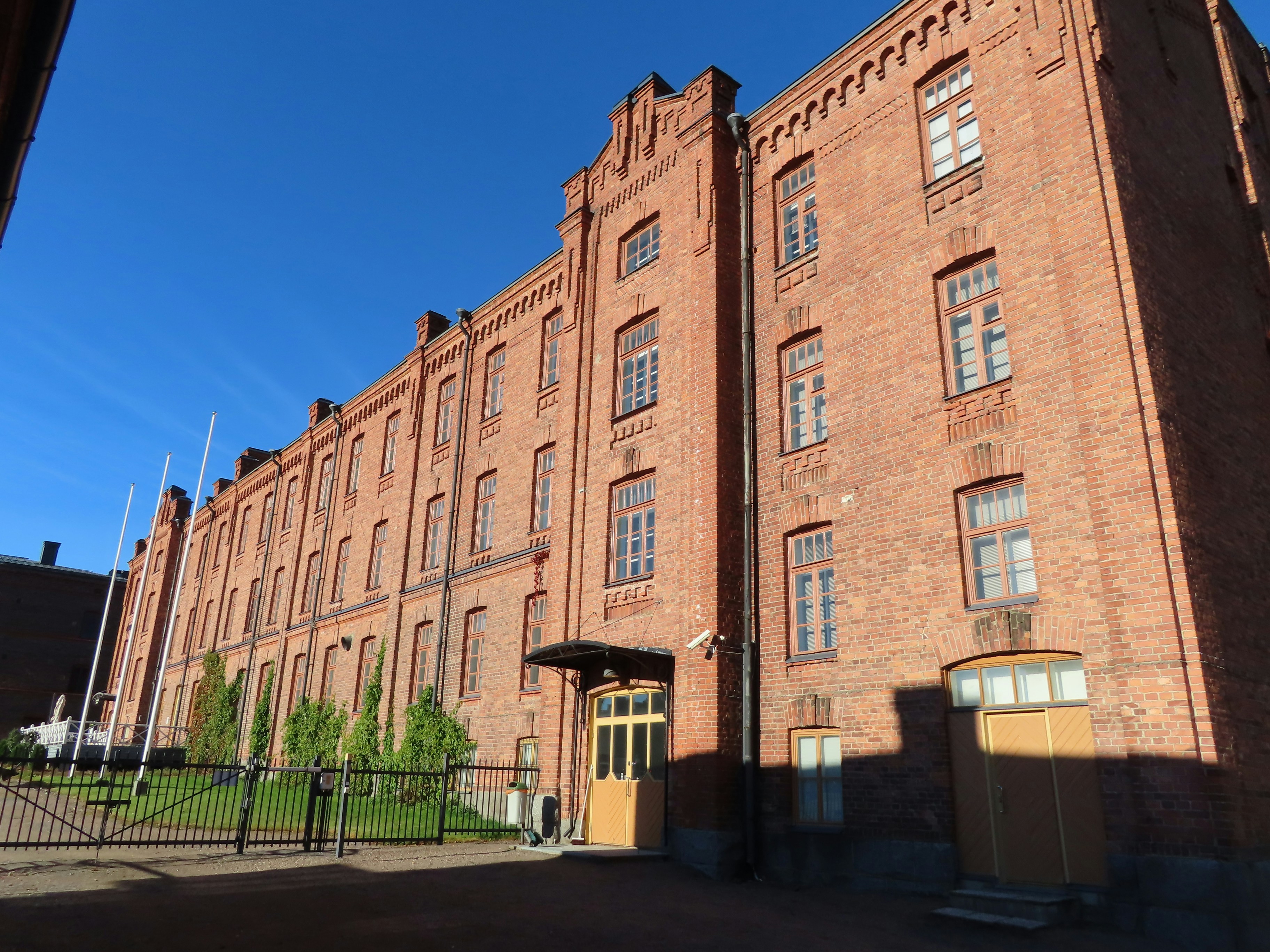 Red brick building with tall windows under a clear blue sky, capturing morning light.