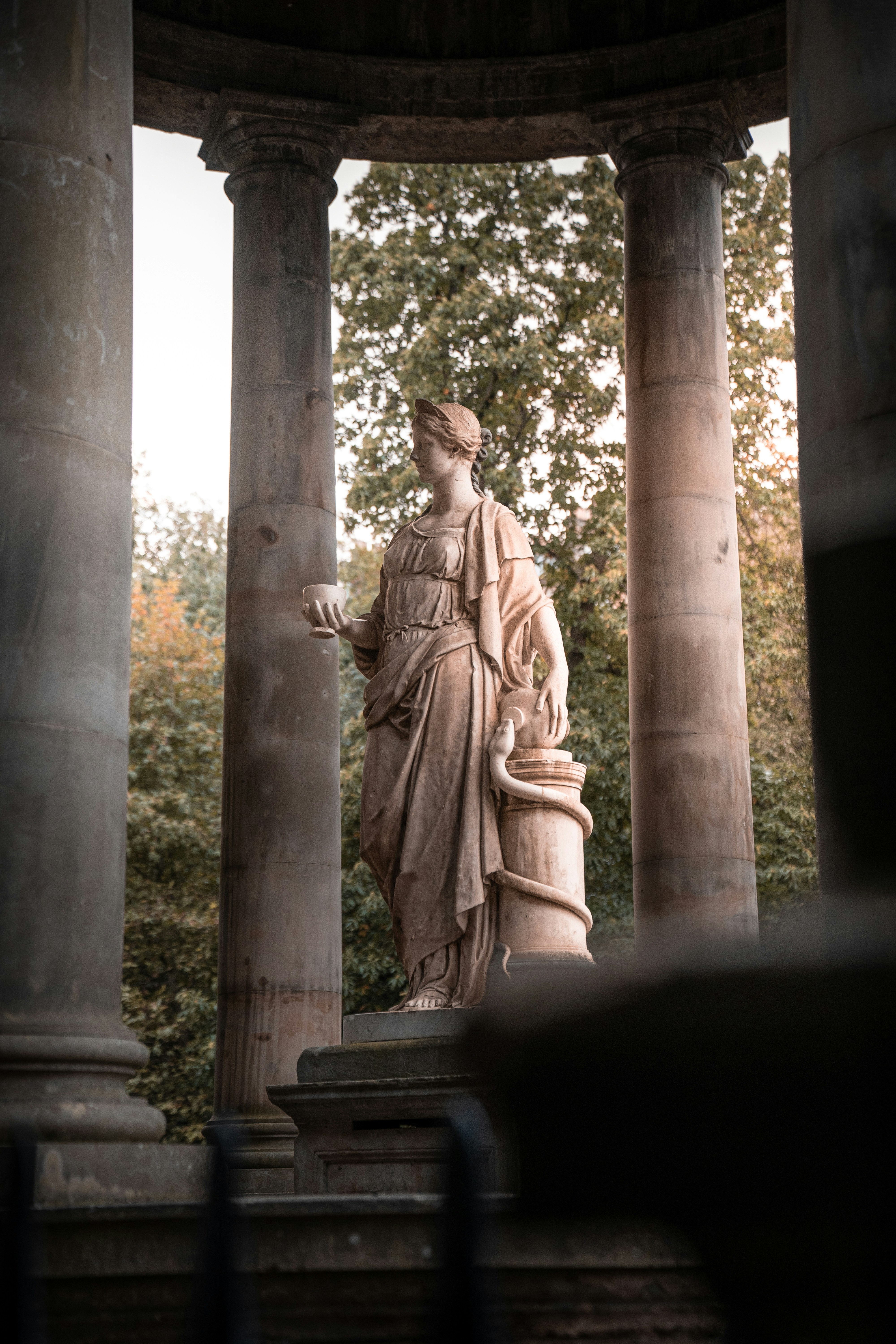 Whispers Between Stone Columns: A Colonnade Statue in Autumn Light