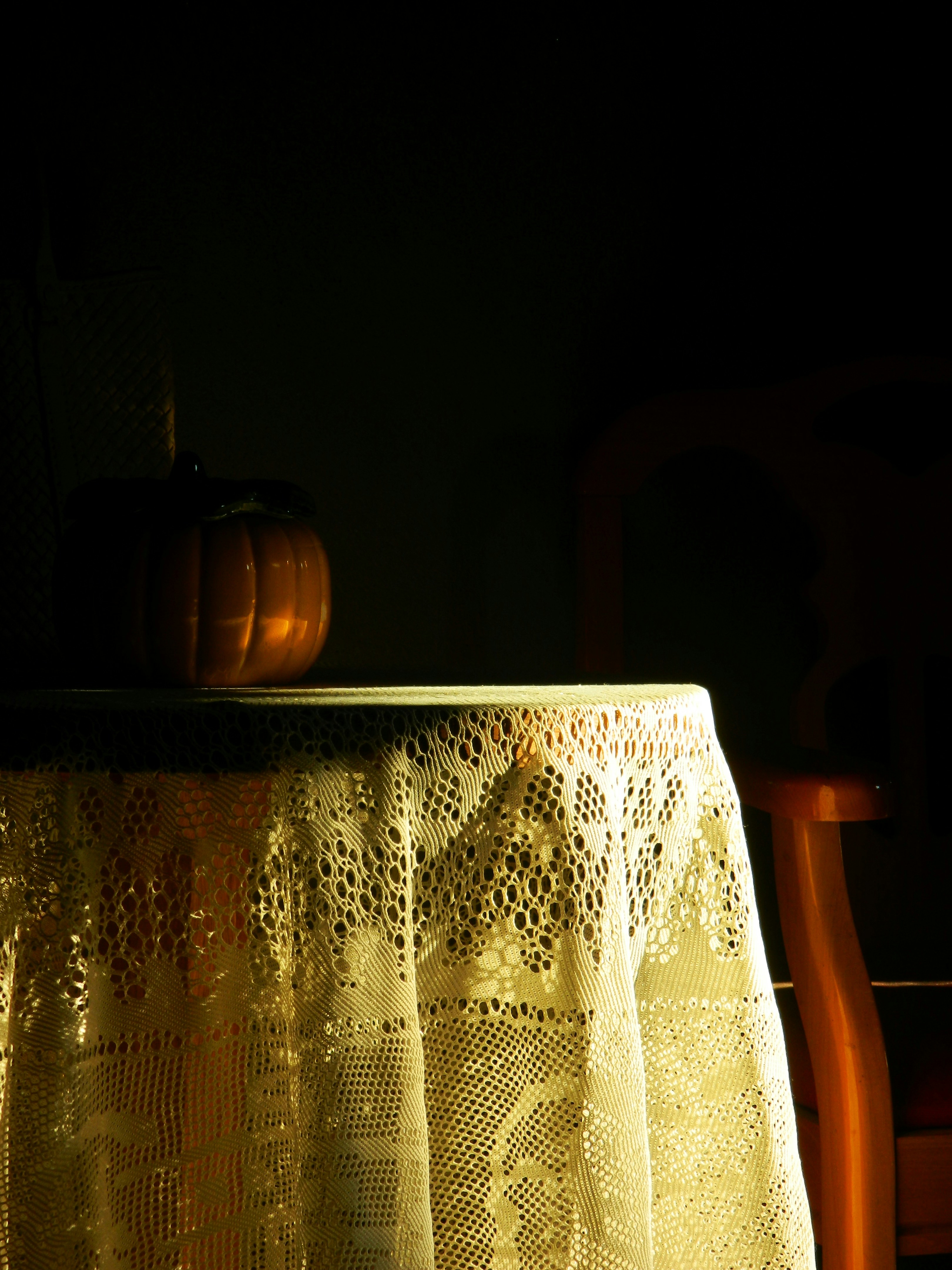 A warmly lit pumpkin rests atop a lace tablecloth, casting delicate shadows in a dimly lit room.