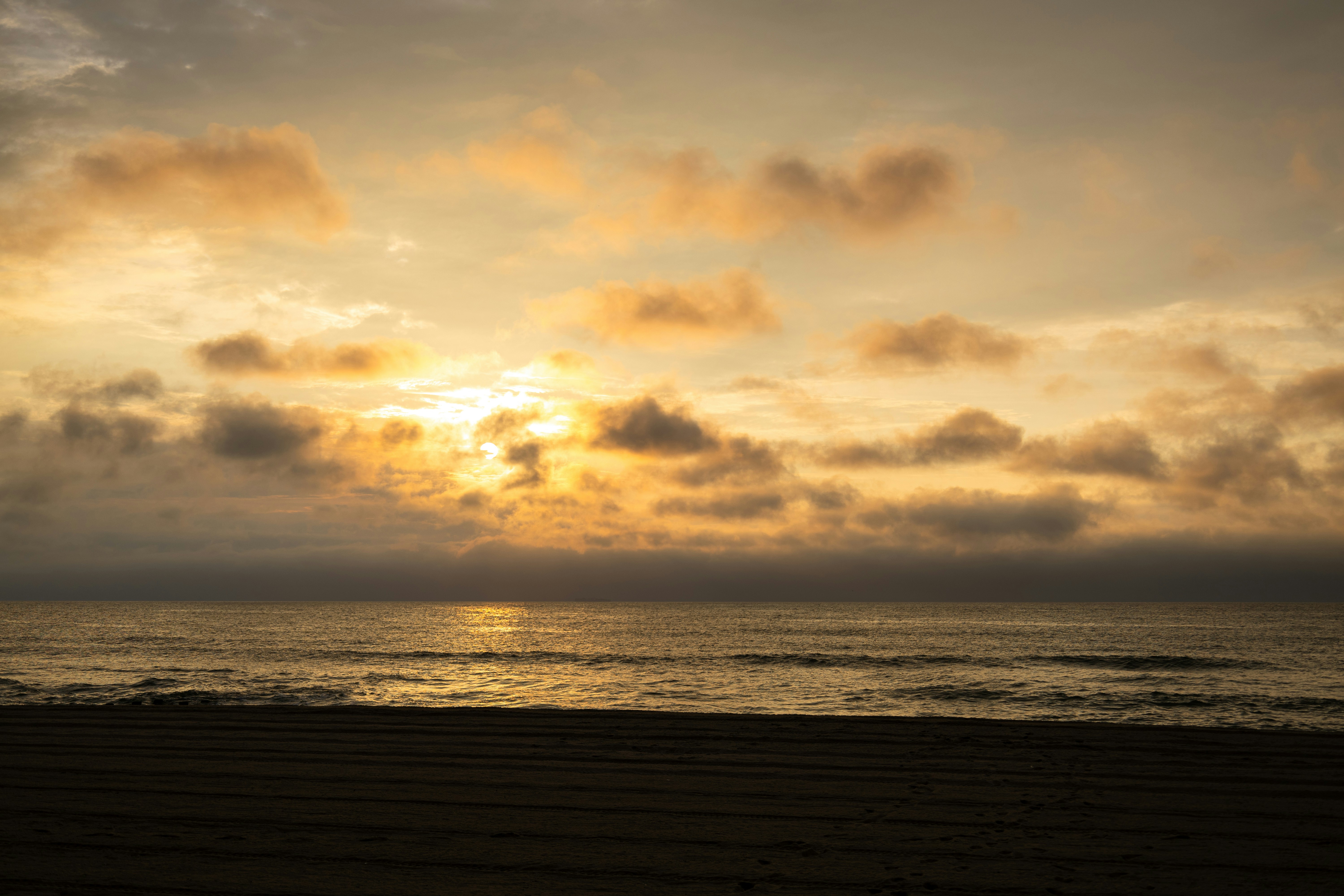The sun is setting over the ocean on a cloudy day