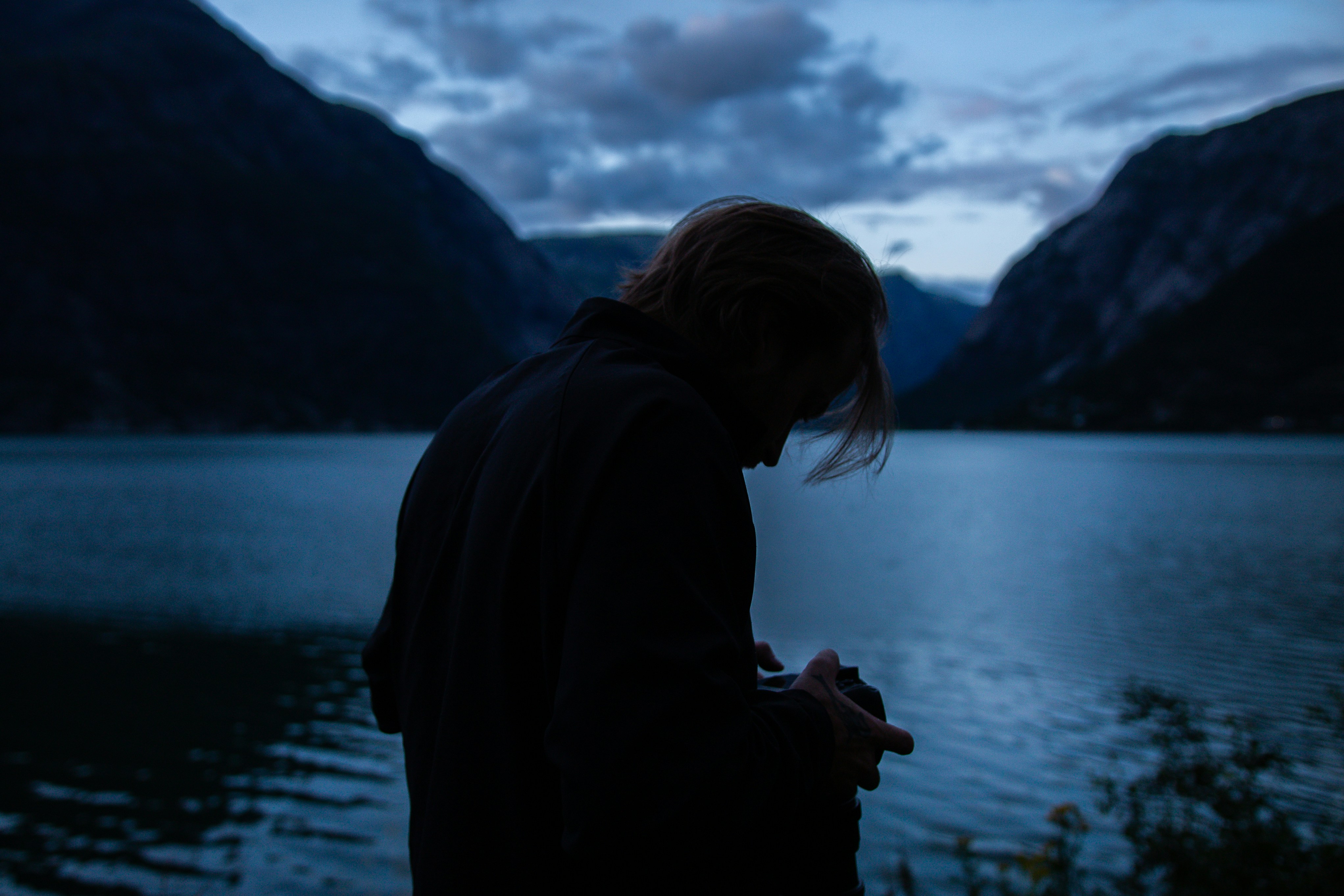 Silhouette of a person looking at a camera by a serene fjord at twilight.
