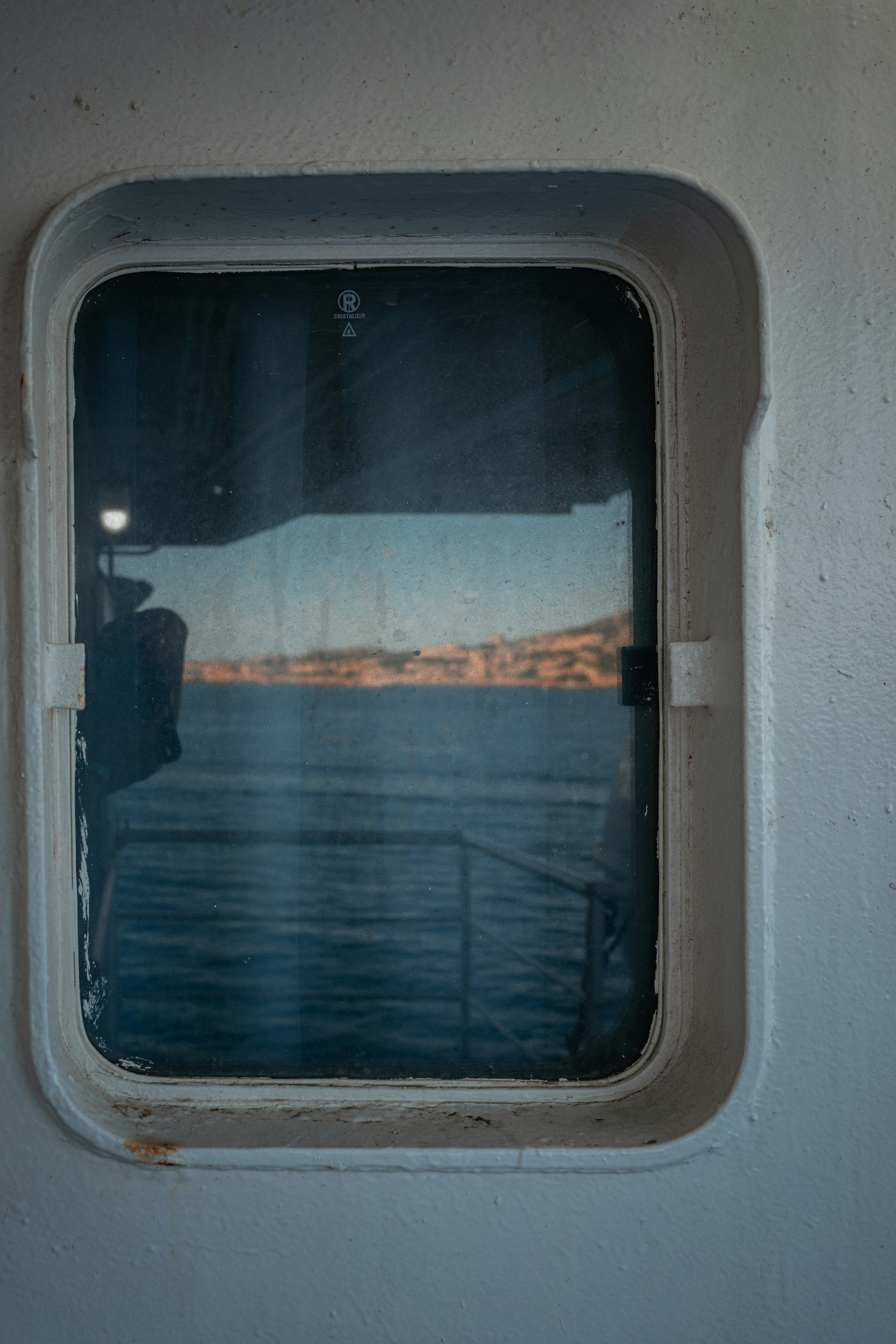 Porthole Reverie: Coastline Through Weathered Glass