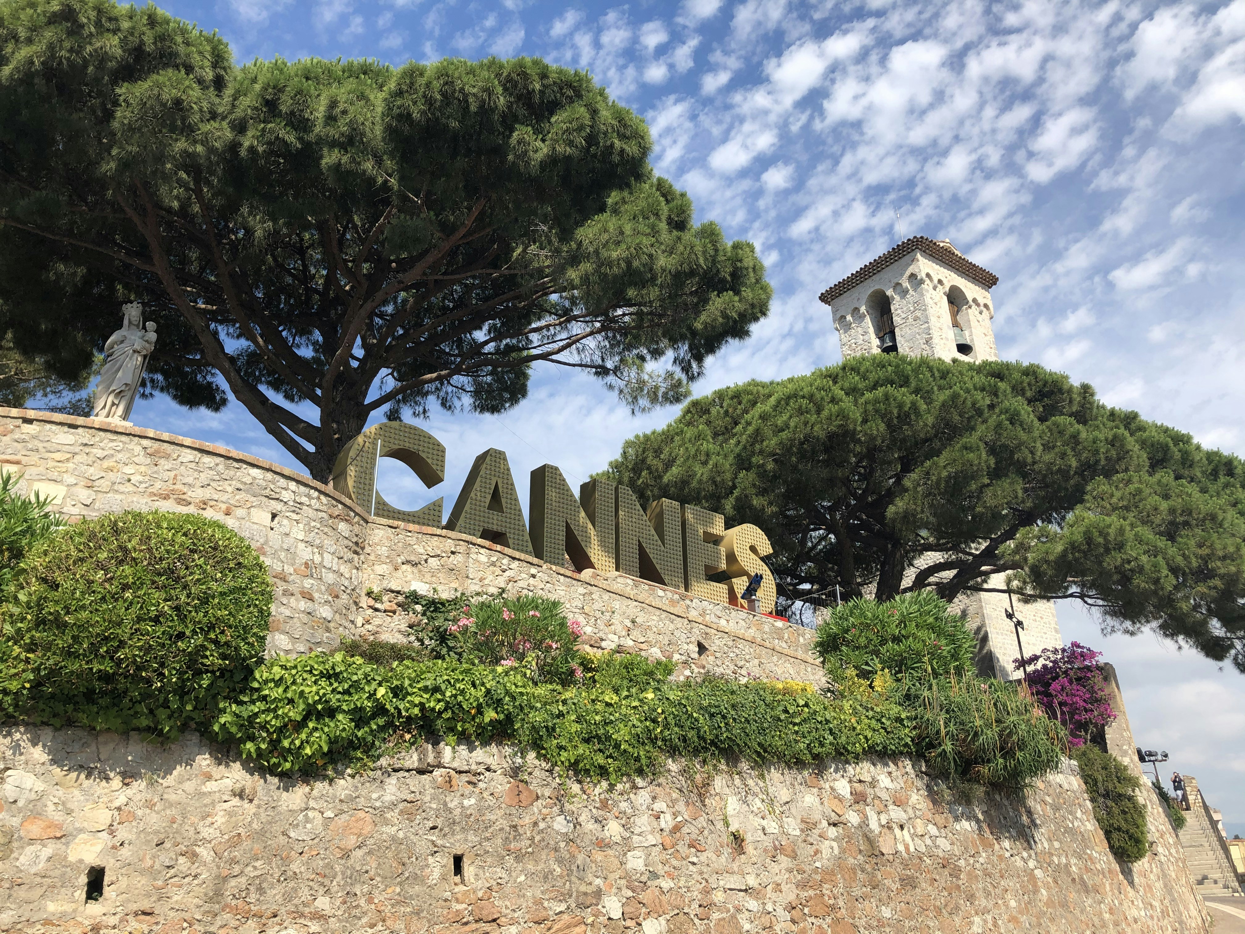 Prominent 'Cannes' sign amid lush greenery and historic architecture, showcasing the coastal allure of the French Riviera.