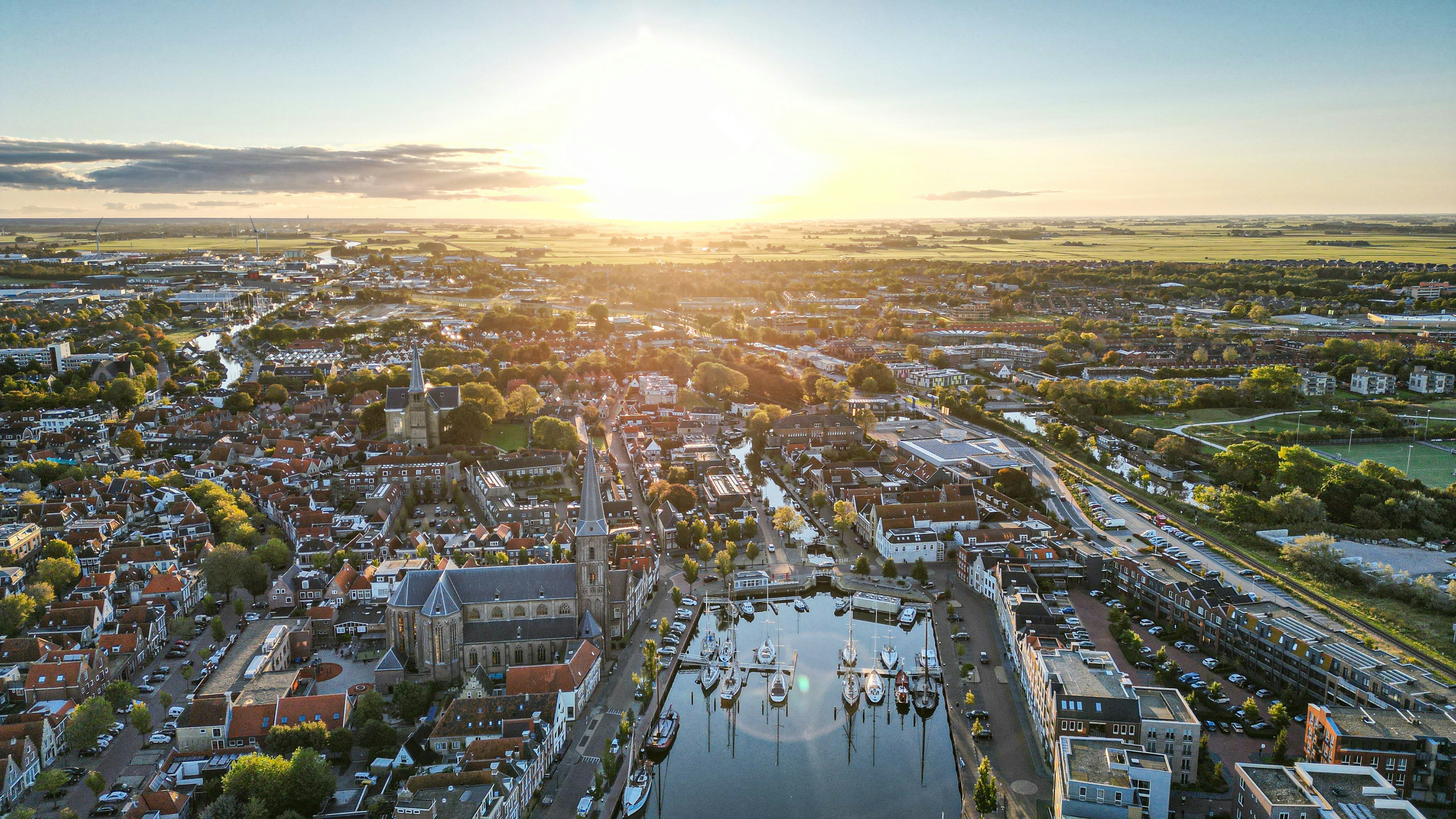 Aerial view of a city and harbor under a setting sun, casting long shadows and illuminating the landscape.