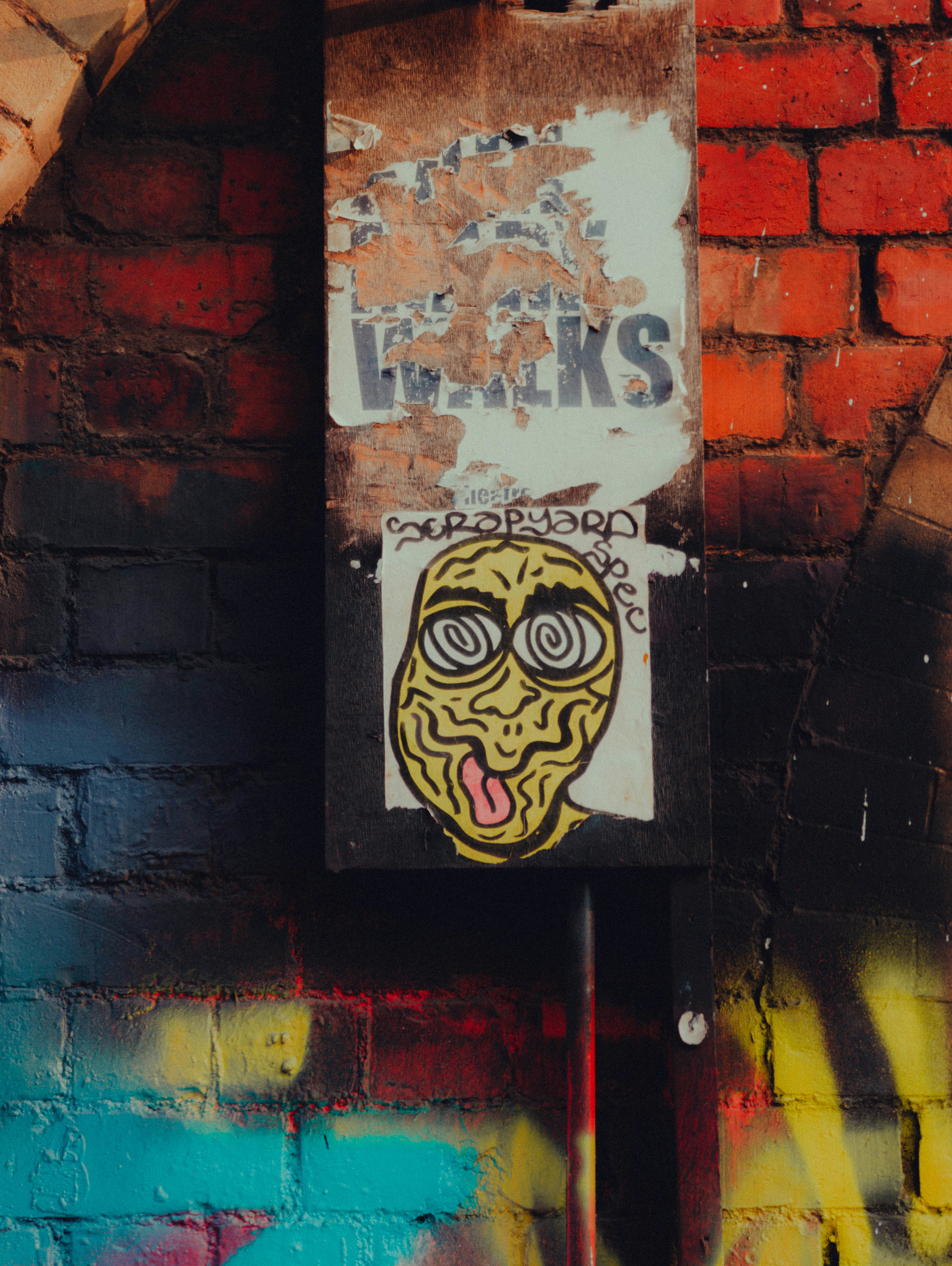 Yellow Mask Sticker Anchored to a Weathered Panel Beneath Urban Graffiti