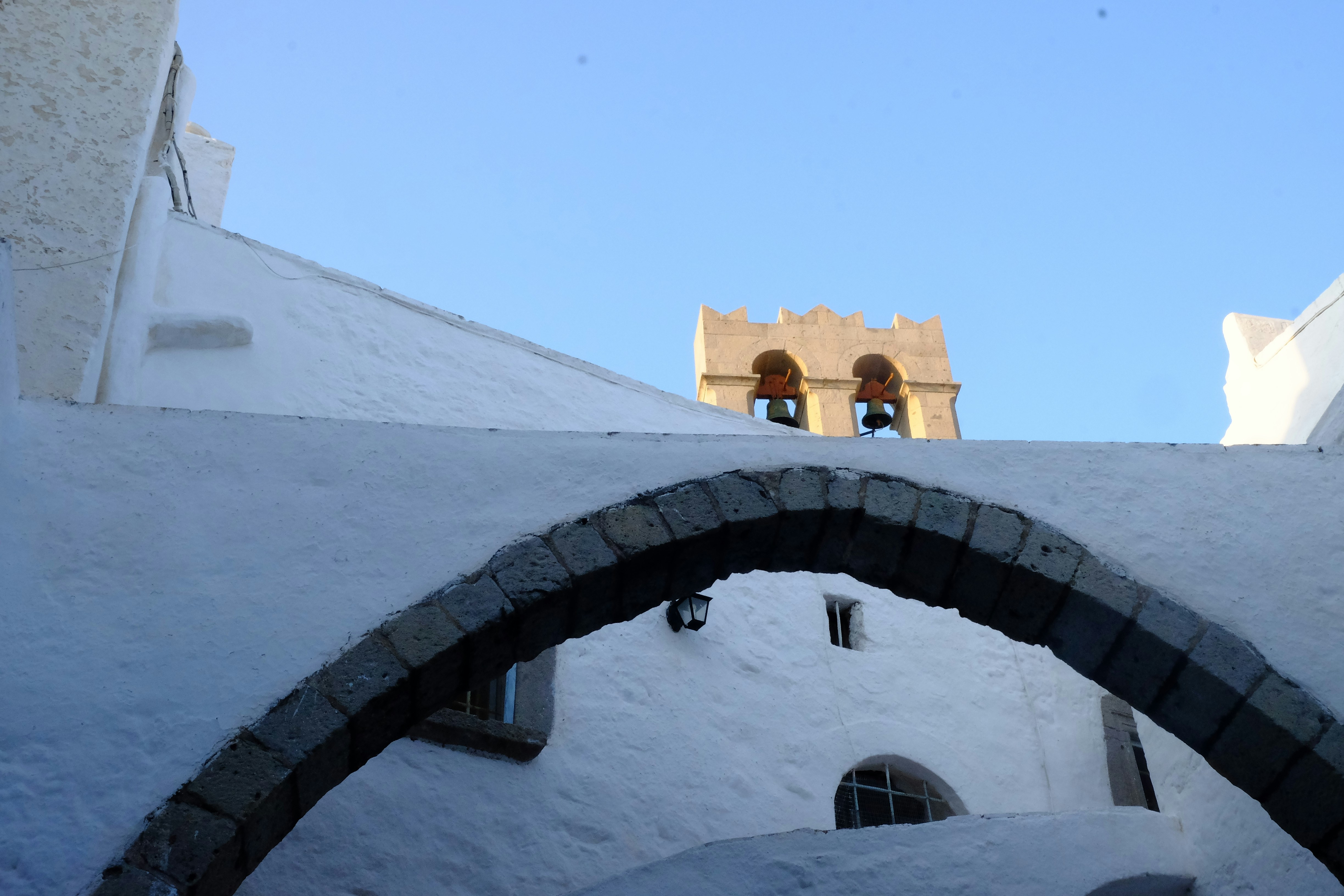 Two Bells Above the Arch: Sunlit White-Walled Courtyard