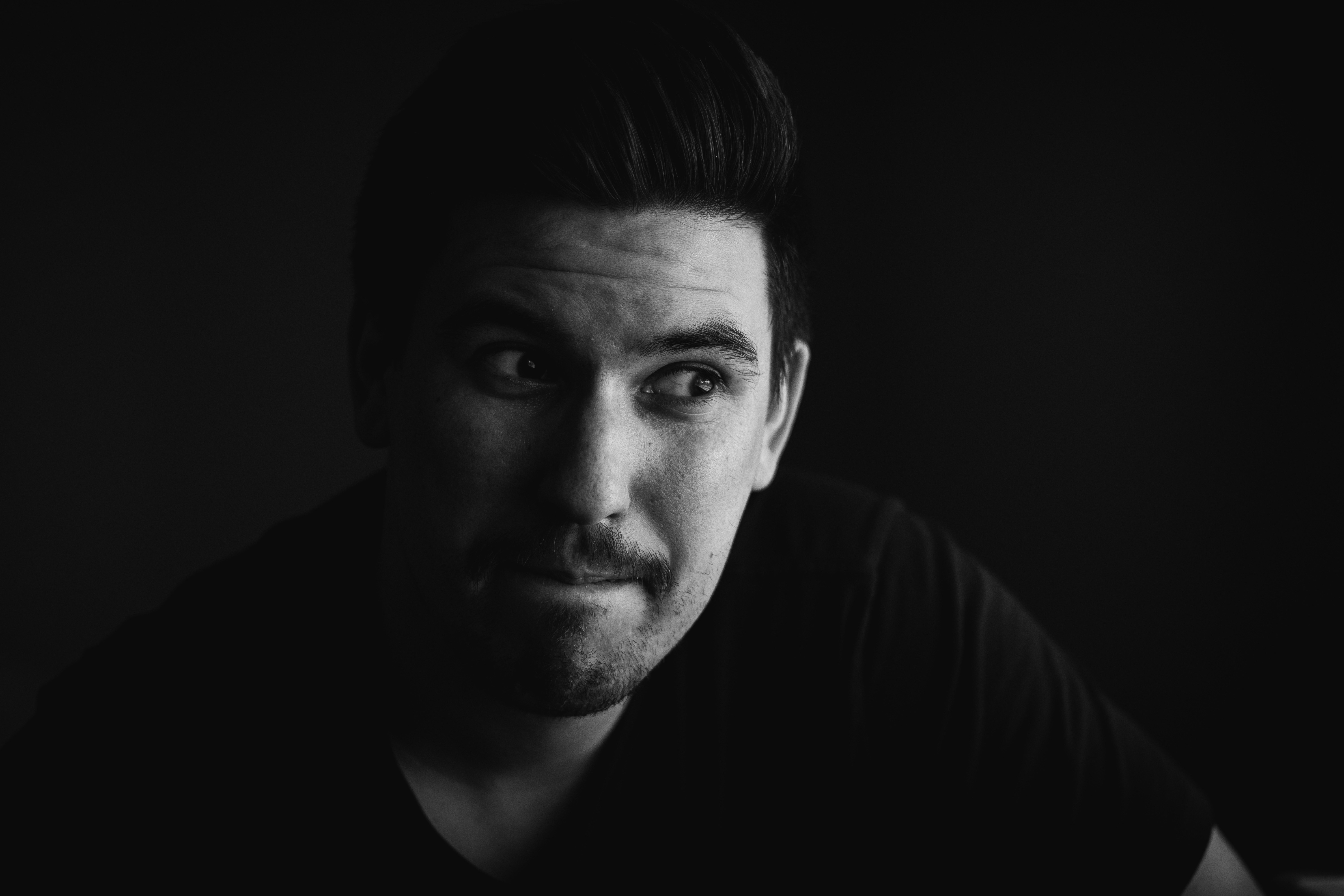 Man in a black shirt gazing thoughtfully against a dark background.