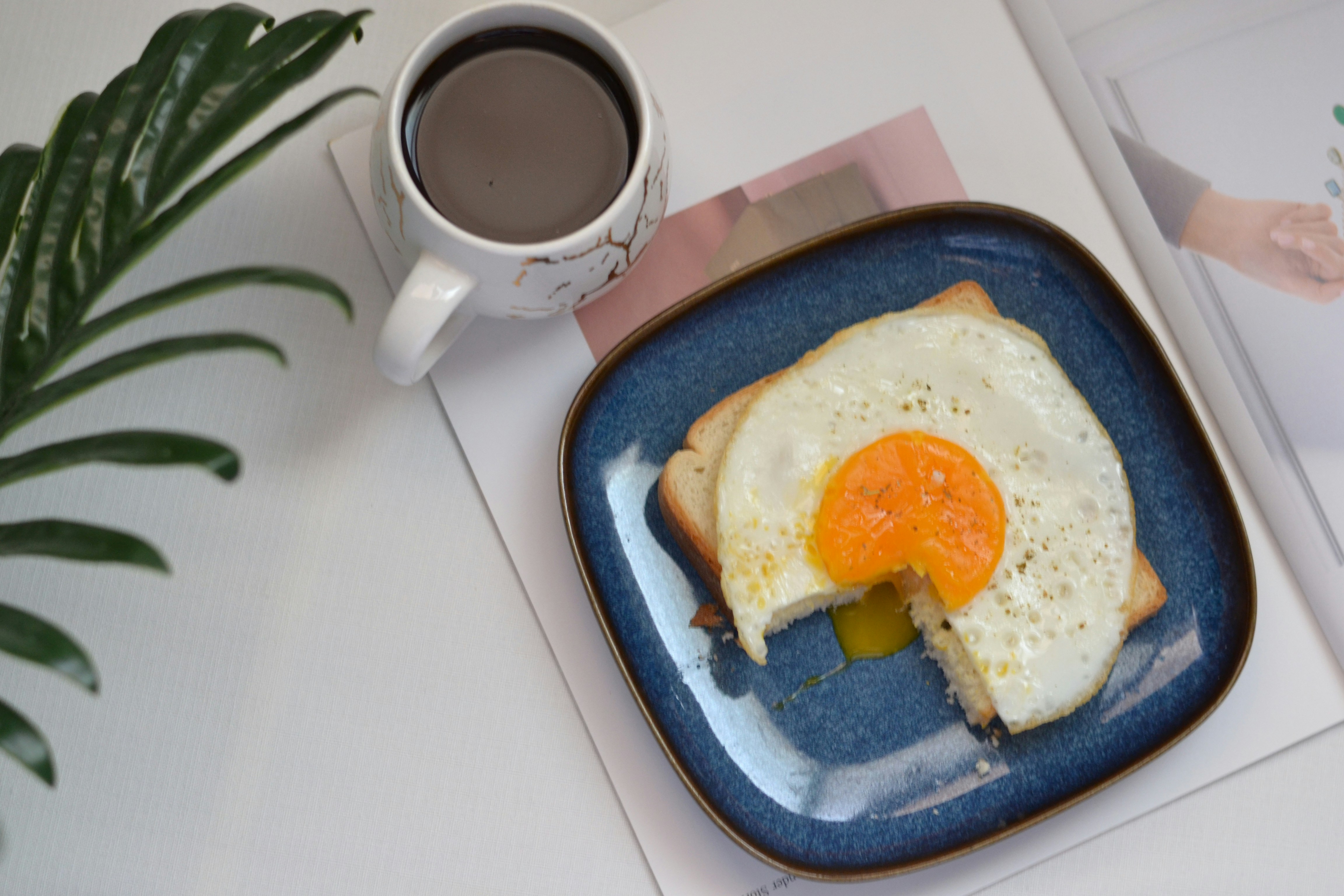 Sunny-Side Focus: Egg on Toast Resting on a Deep Blue Plate with Morning Coffee