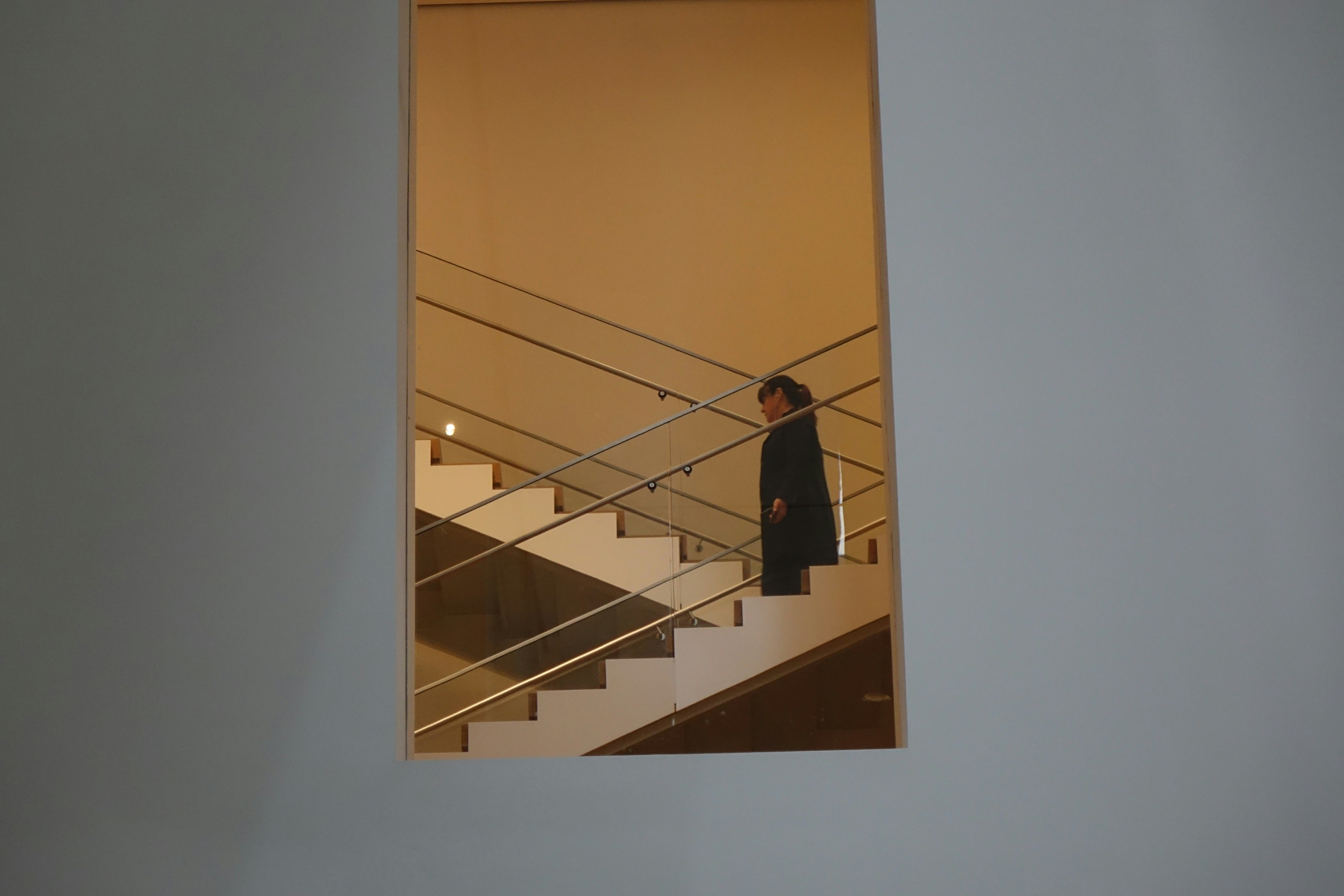 Framed Ascent: A lone suited figure climbs a geometric stairwell through a pale-blue opening