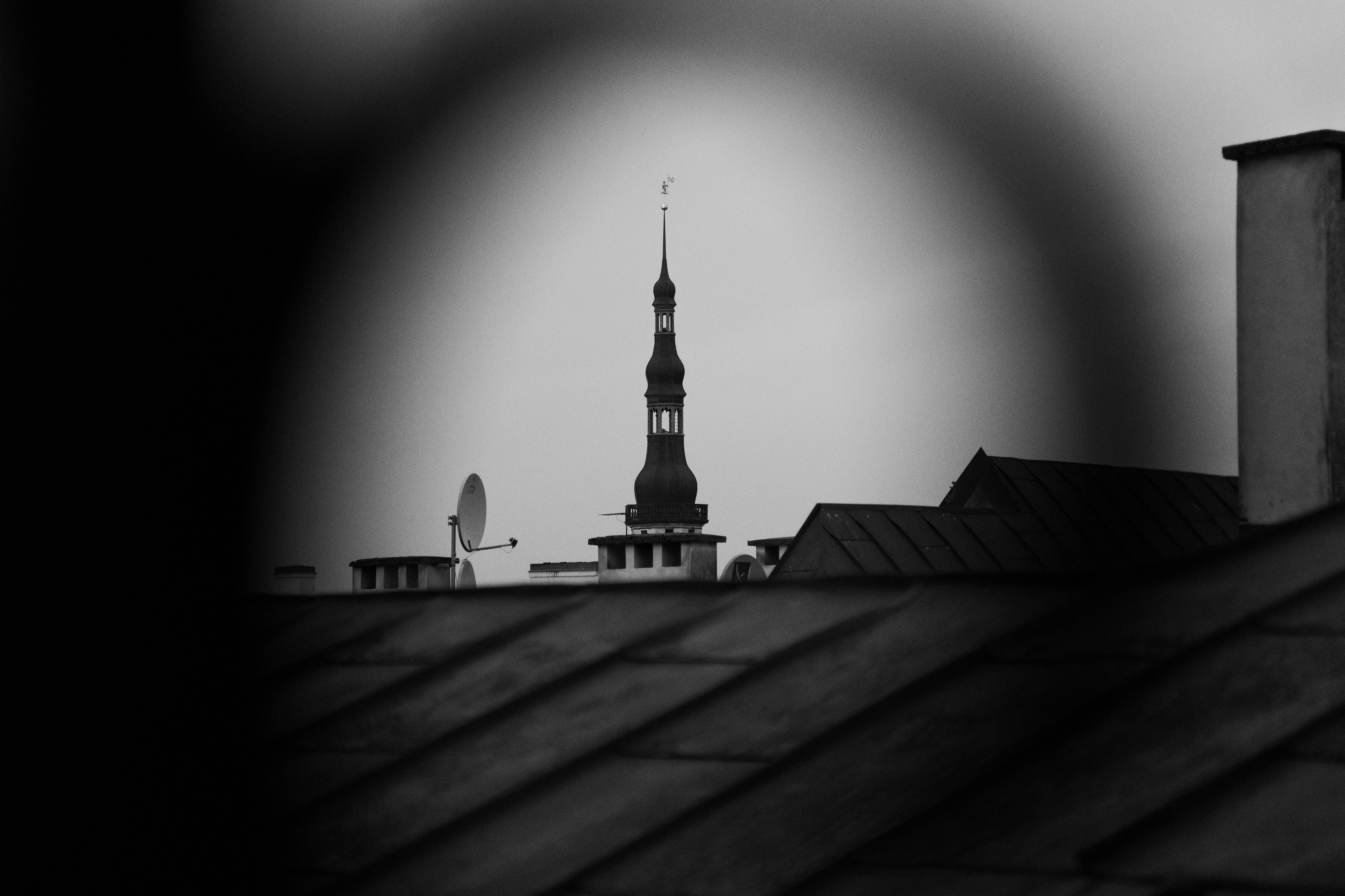 Tallinn town hall spire framed by rooftops and a satellite dish in monochrome.