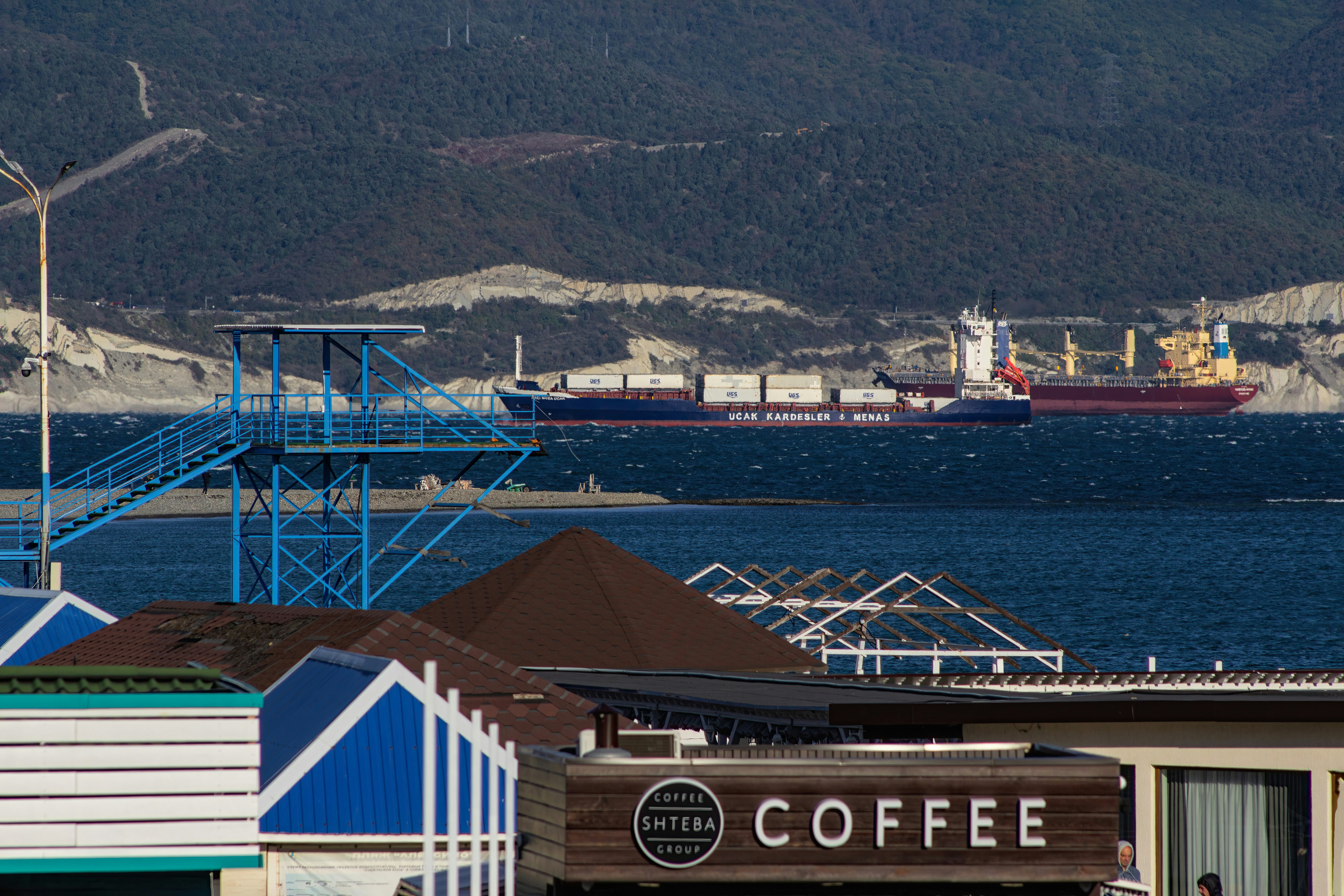 Blue Framework Over the Harbor: Coffee Sign Framed by Cargo Ships