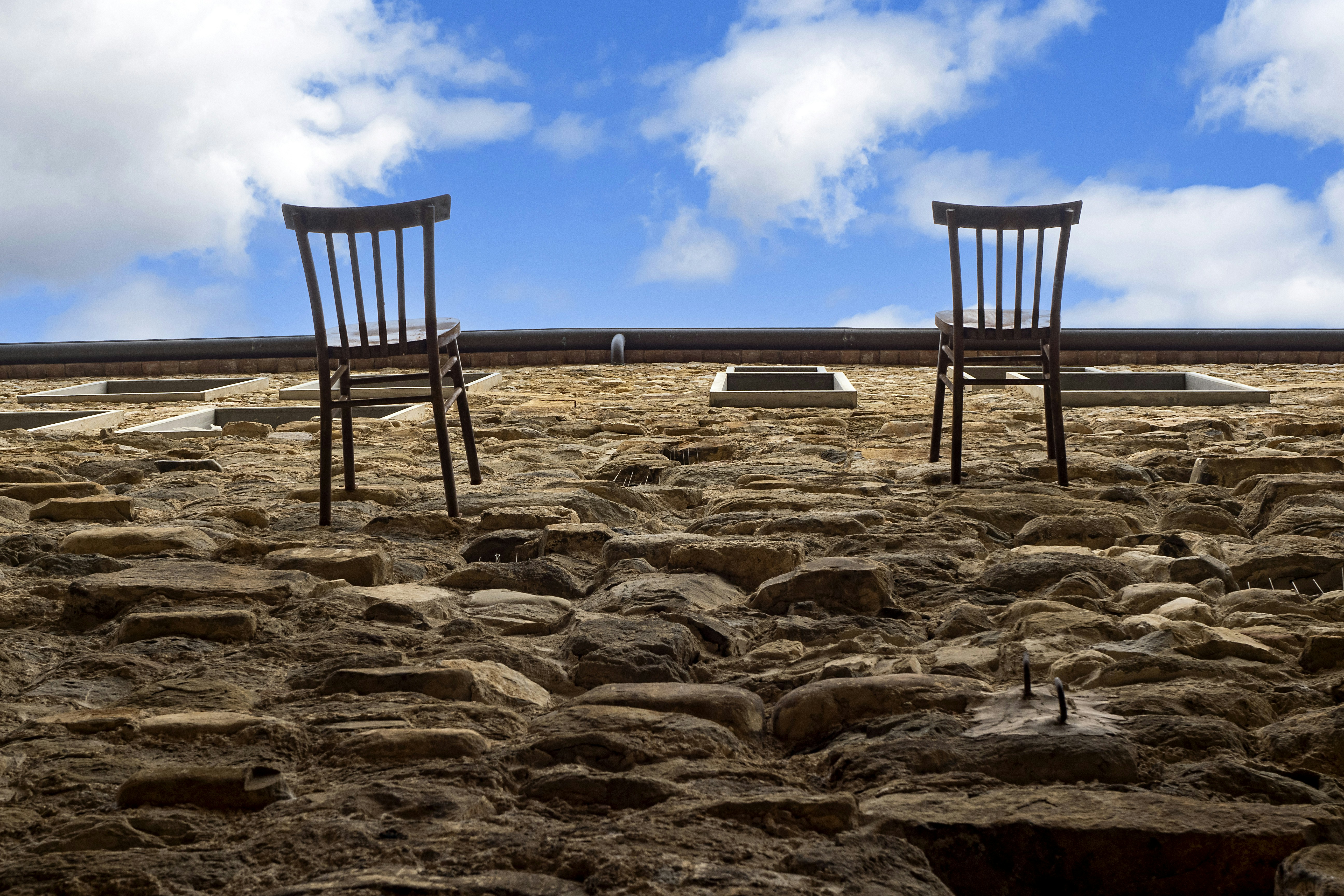 Balanced Repose: Chairs Against a Stone Wall Under Wide Sky