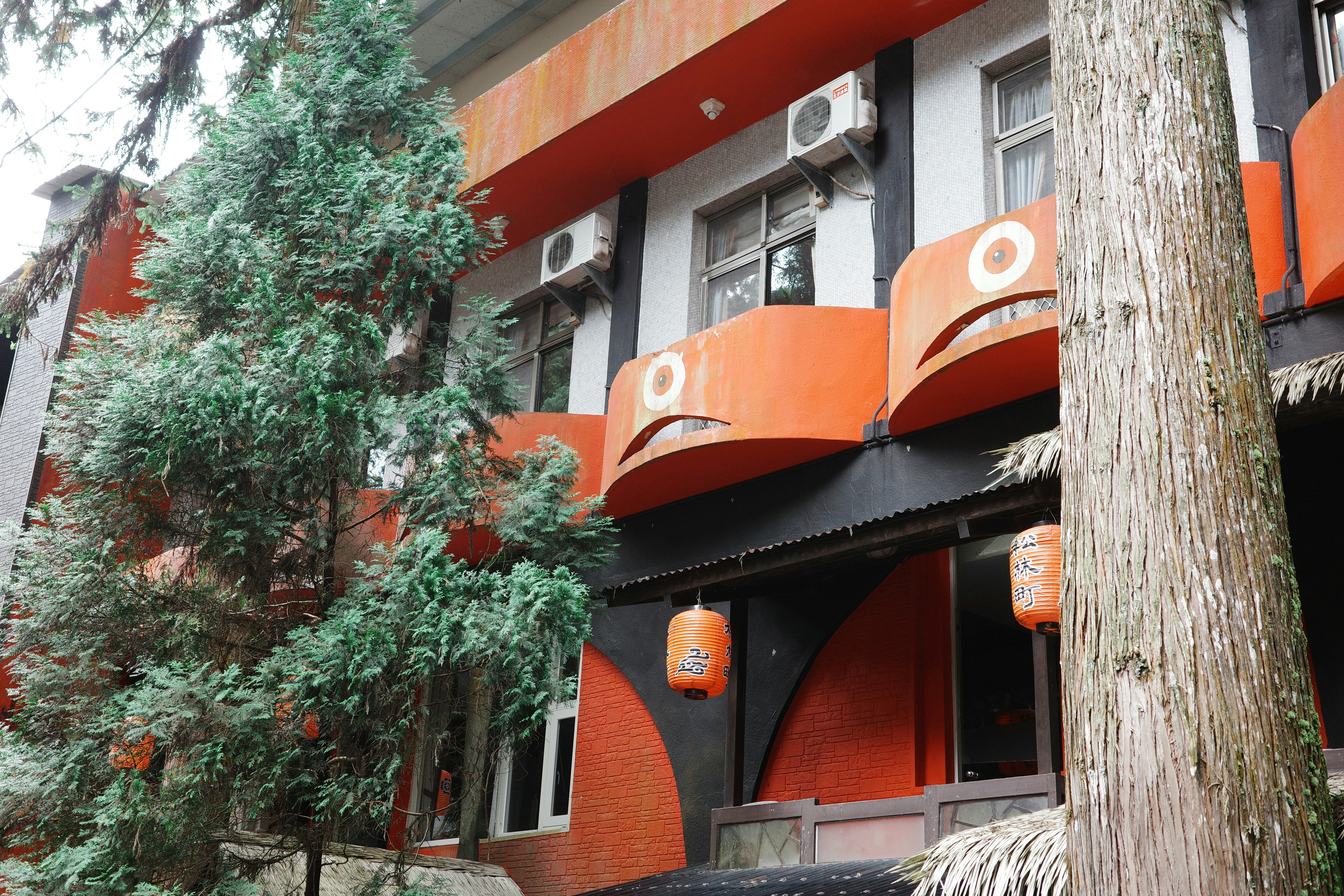 Modern building facade with bold orange accents and lush green trees in the foreground.