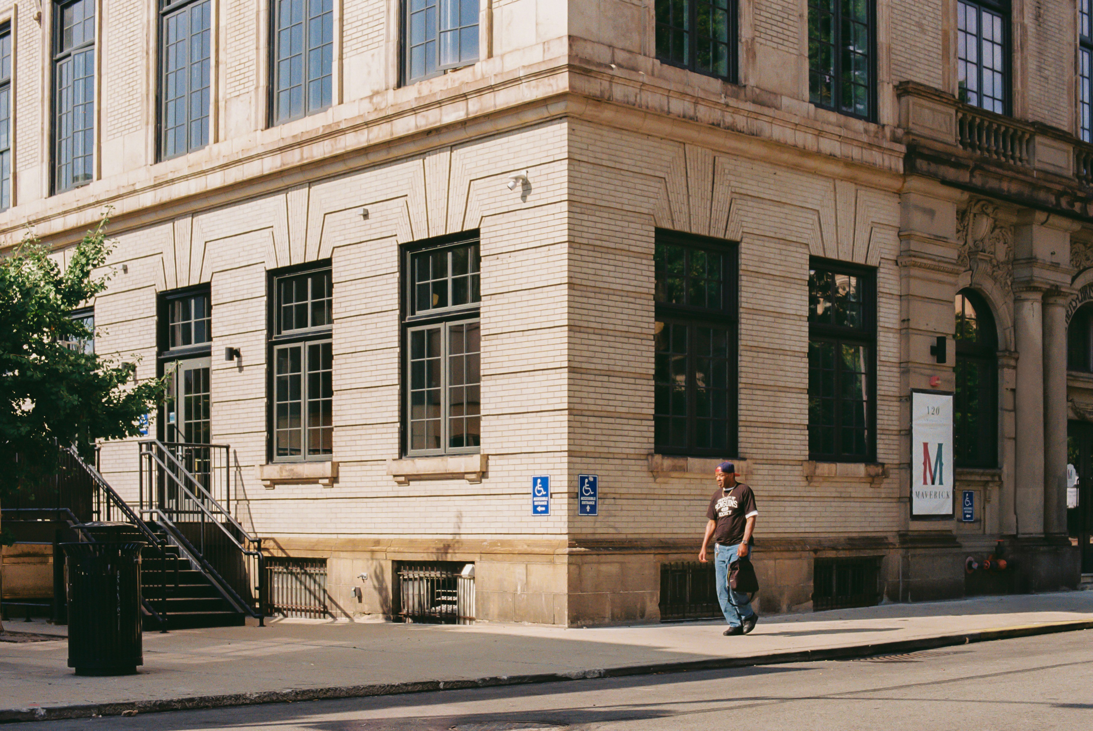 A man walking down a street past a tall building photo – Free Film ...