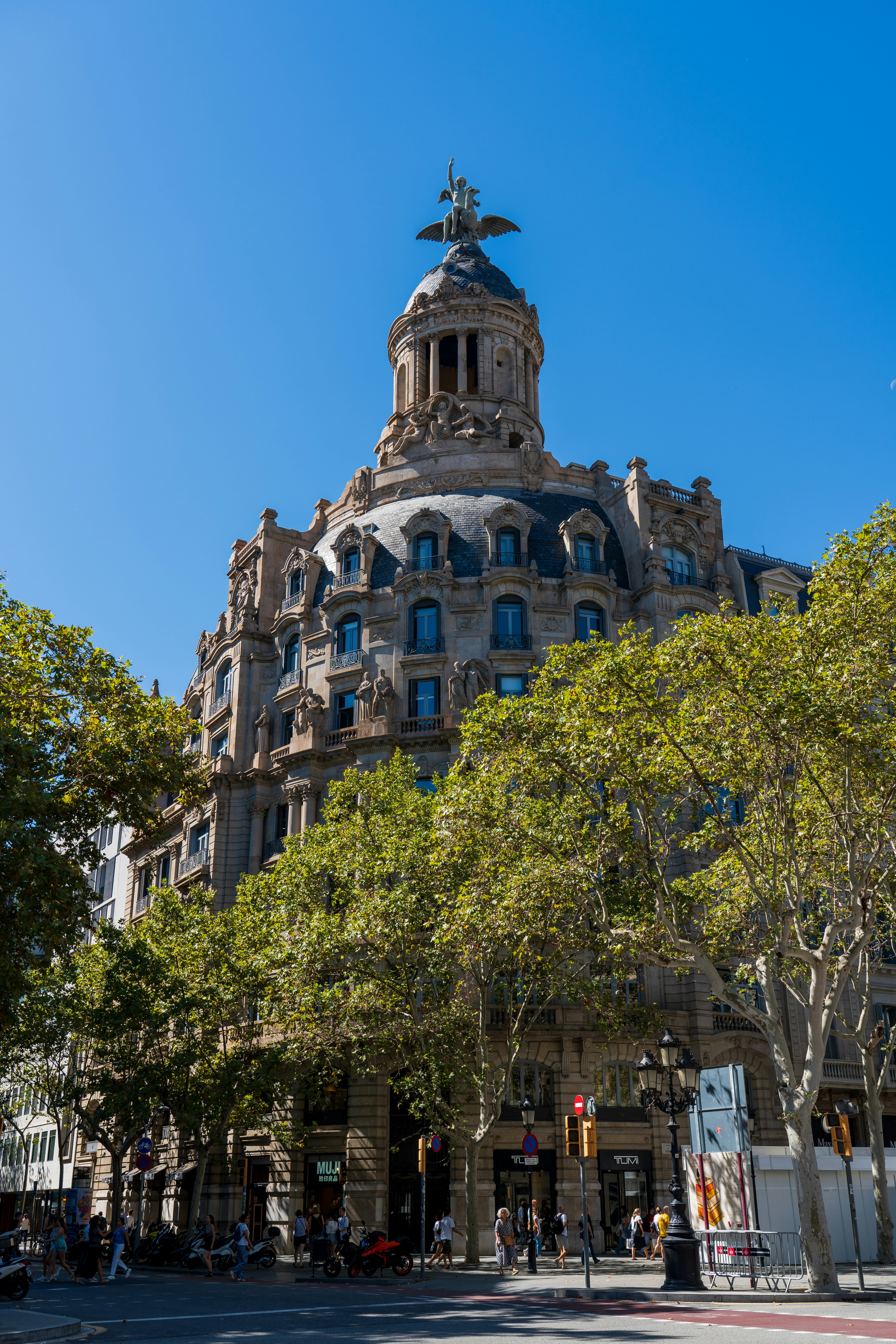 Facade of a grand stone building crowned with a winged statue under a clear blue sky