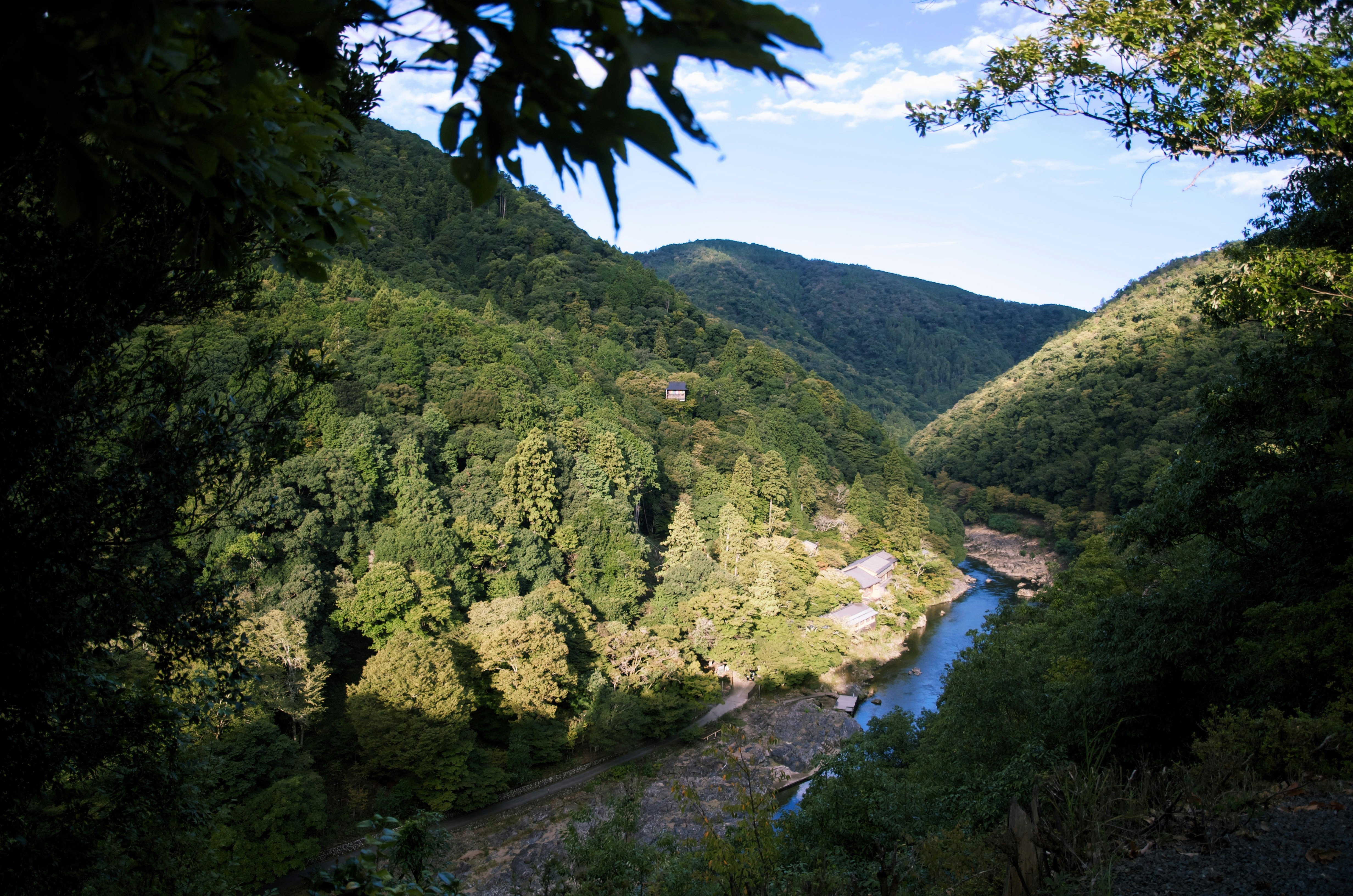 Lush green mountains embracing a secluded river with scattered buildings under a clear blue sky.