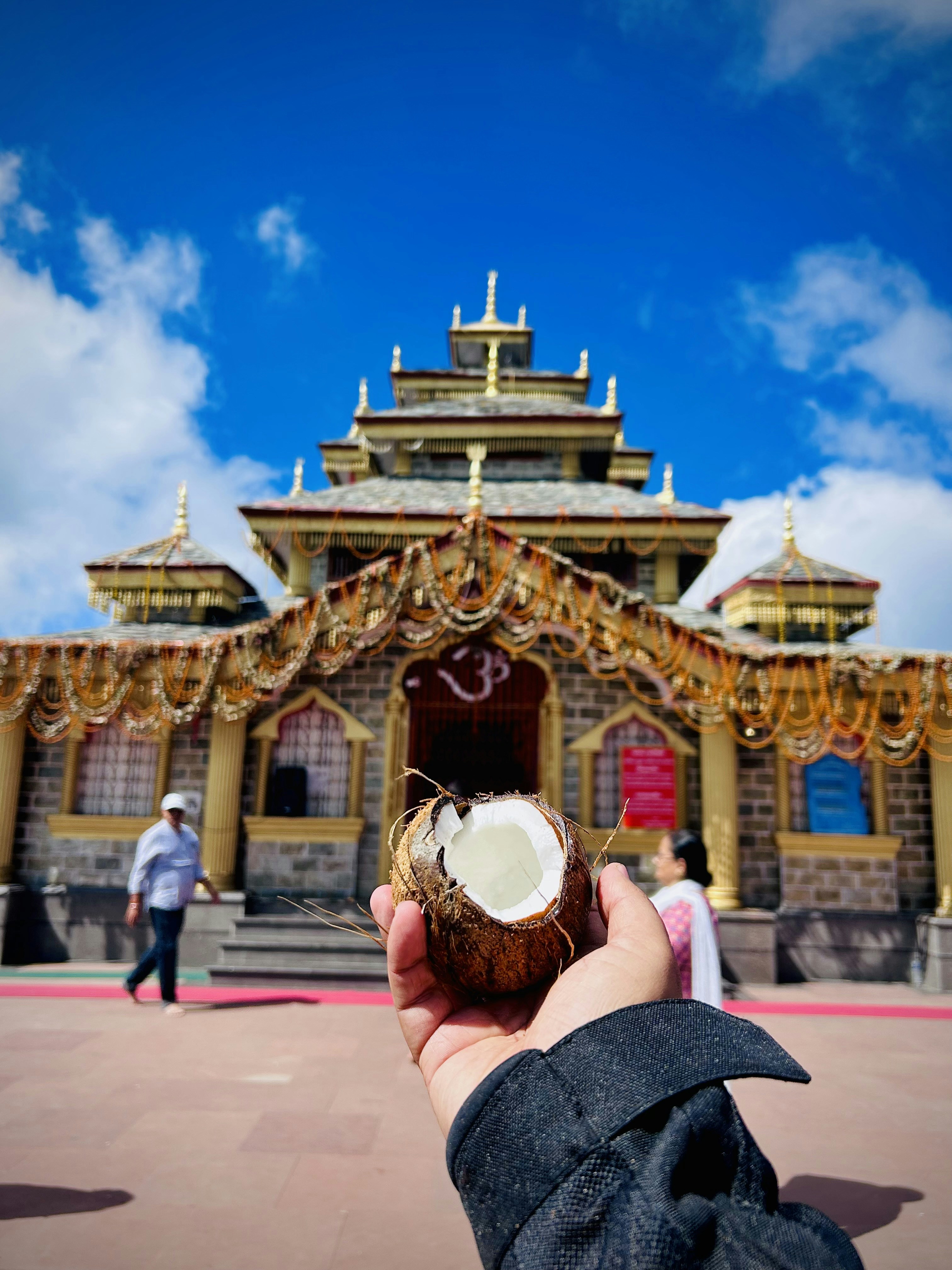Coconut in Hand Framing a Gold-ornate Temple Against a Clear Blue Sky