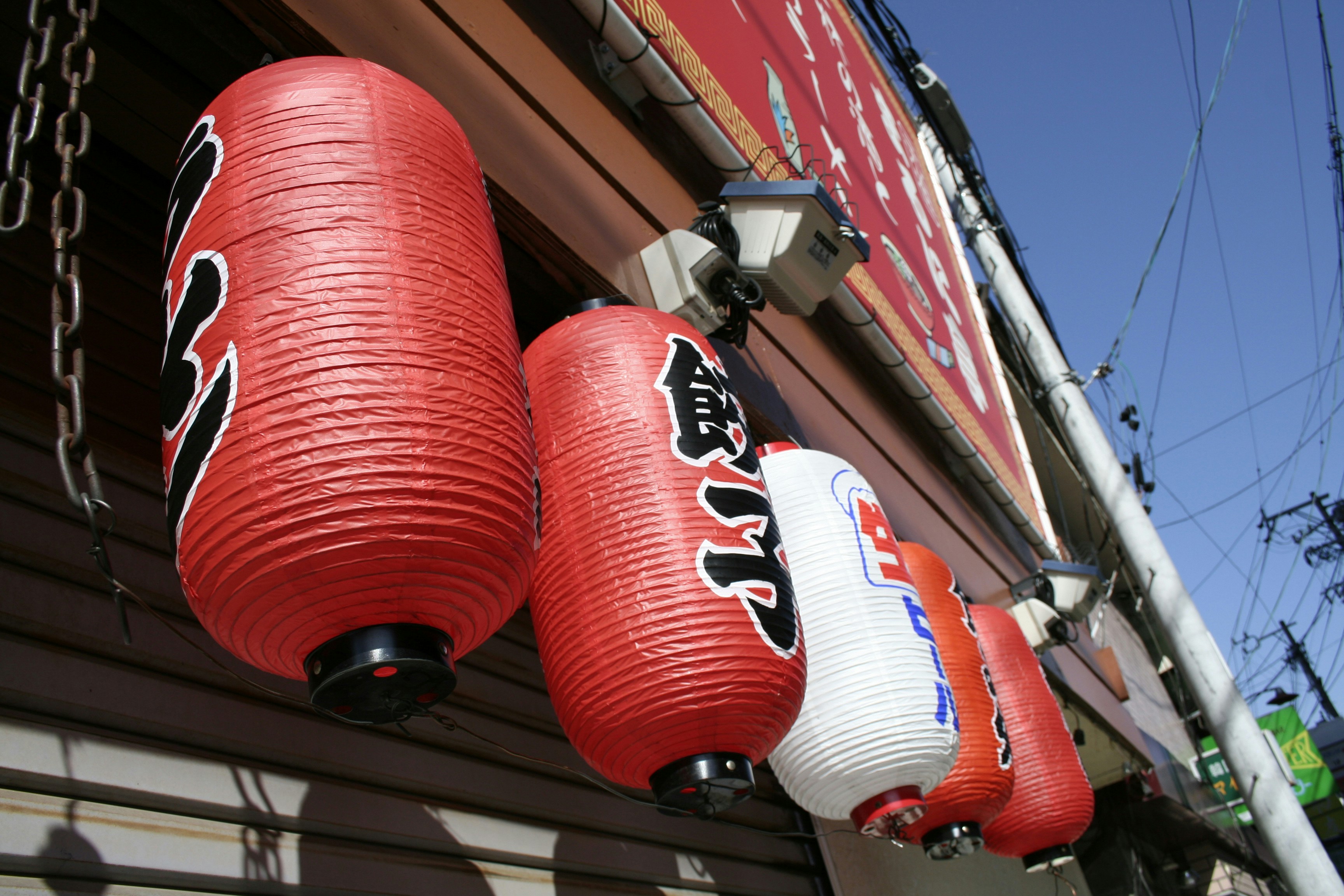 Red and white paper lanterns hanging outside a storefront against a clear blue sky.