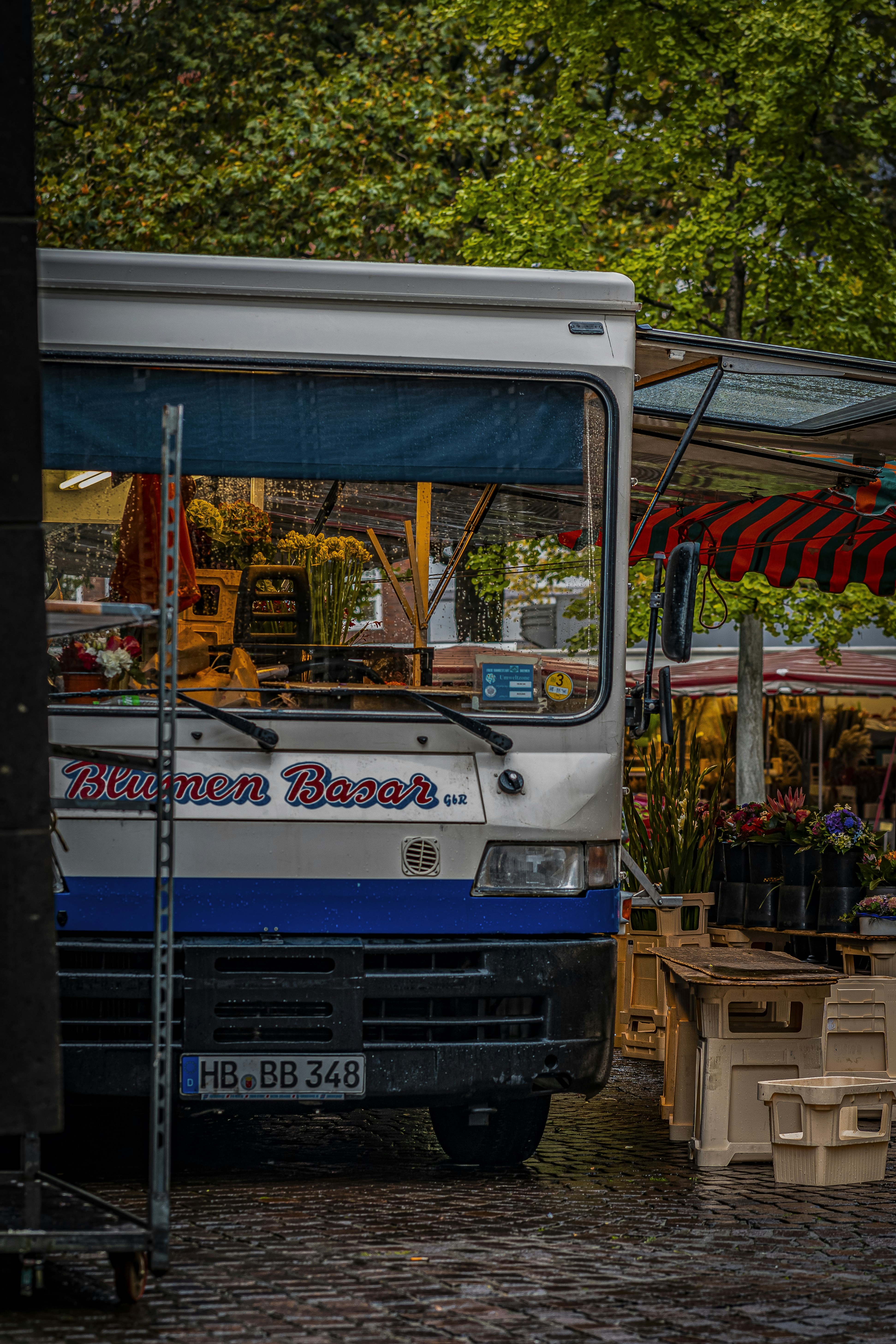 Front Window Bloom: A Flower Market Bus Amid Crates and Cobblestones
