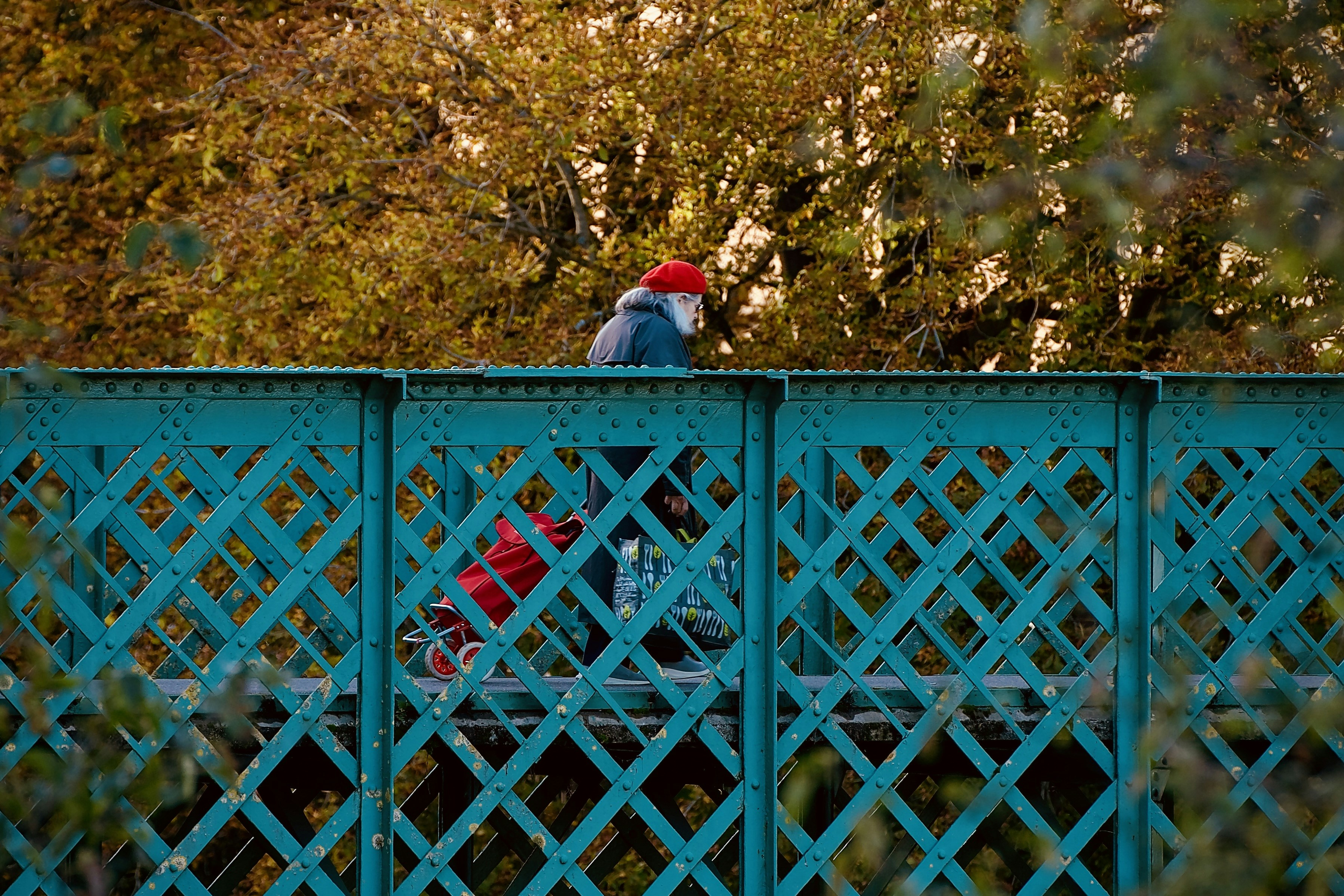 Red-capped traveler crossing a teal lattice bridge beneath autumn light