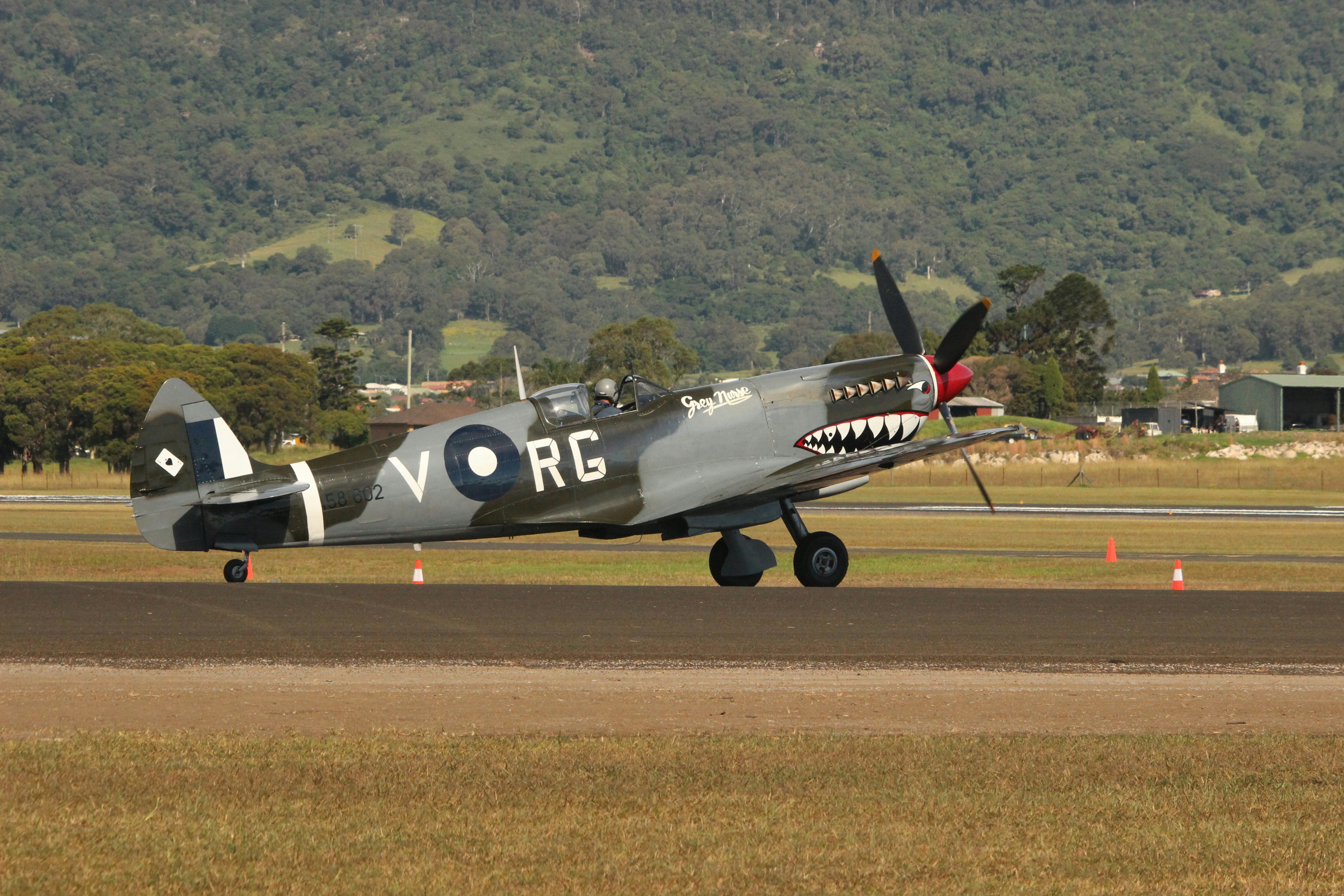 Historic Spitfire aircraft on a runway with distant hills in the background.