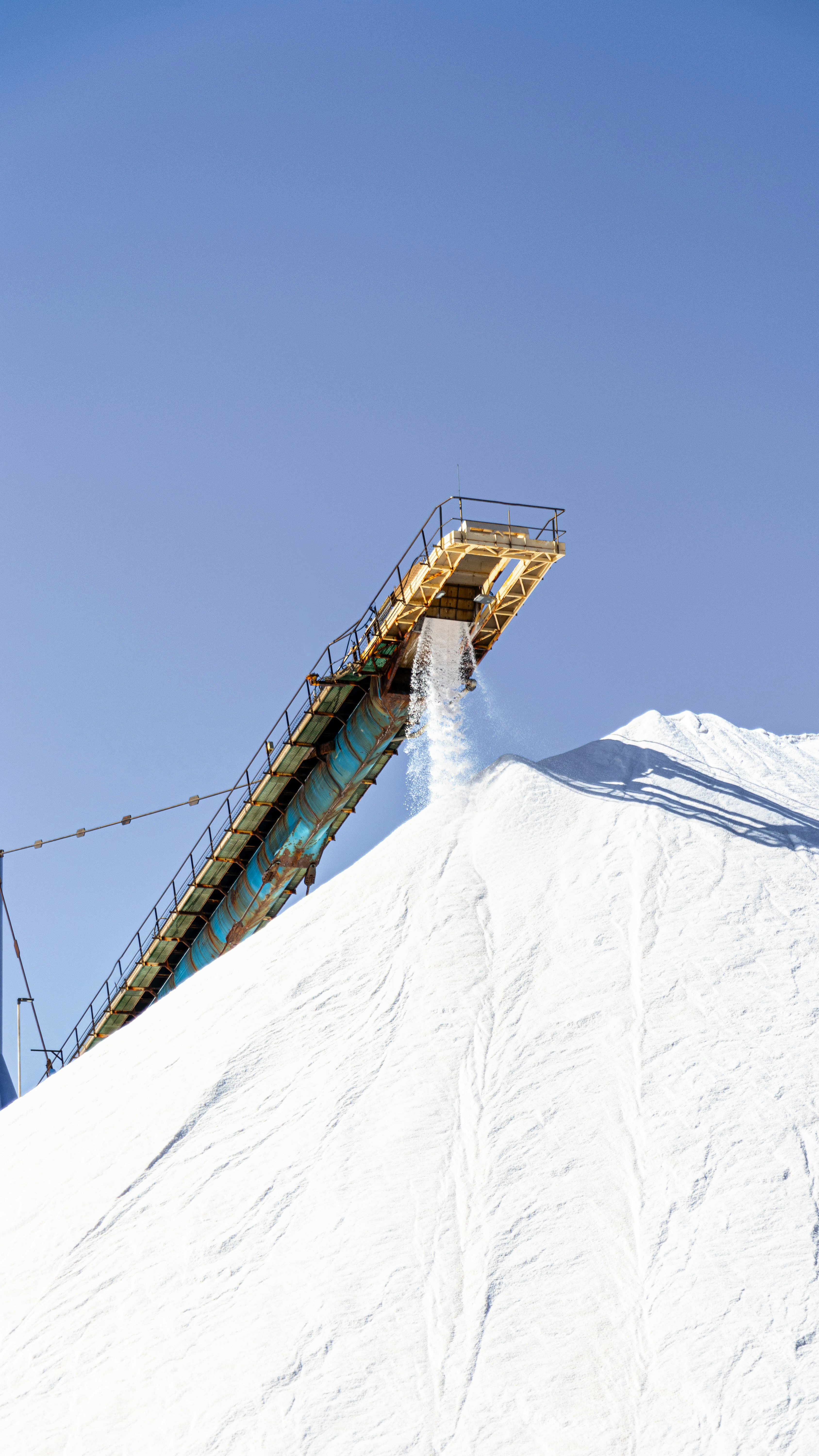 Powder Cascade from a Snow-Handling Conveyor Under a Clear Alpine Sky