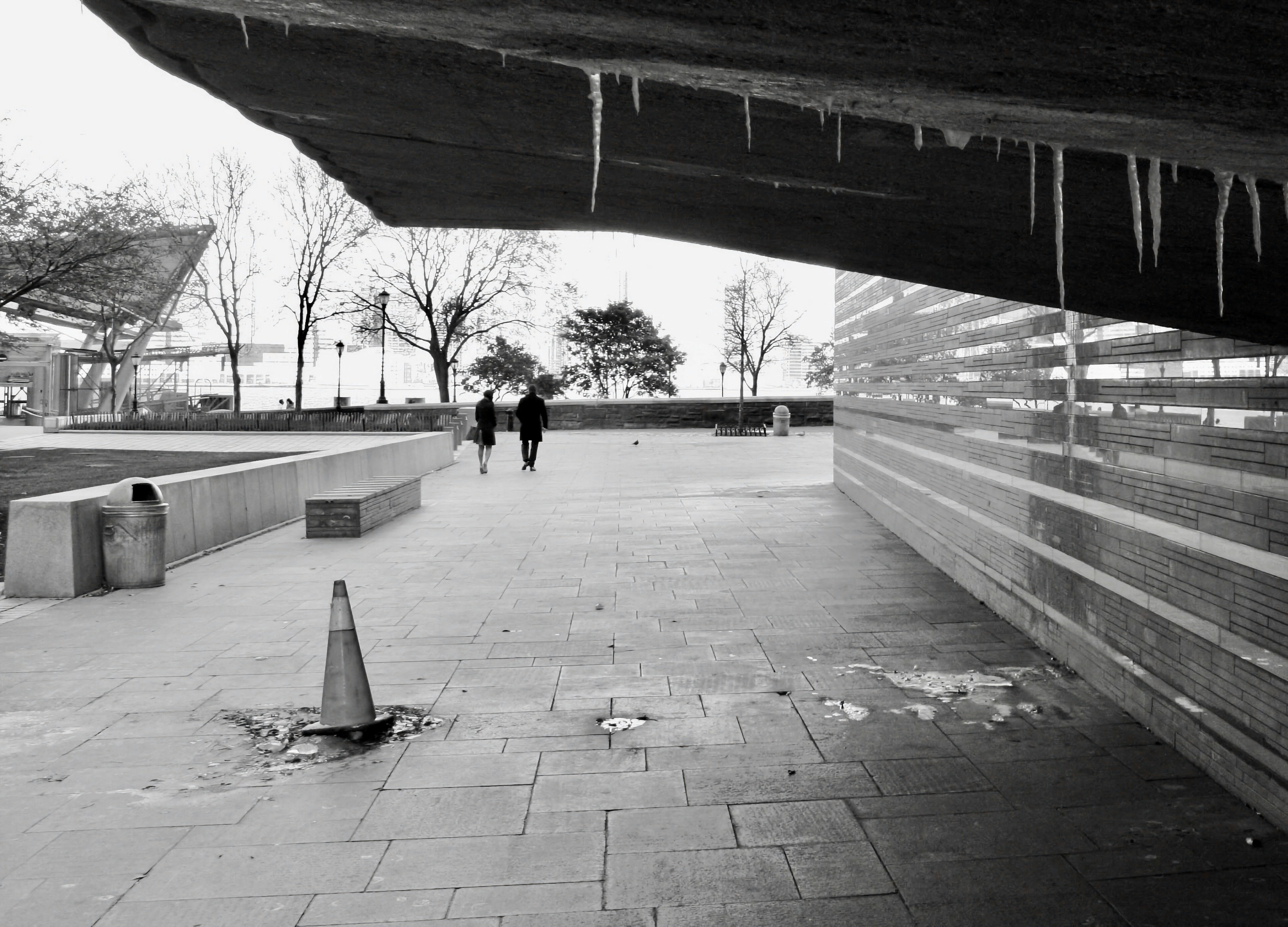 Crossing Quiet: Two Figures in a Stark Winter Plaza Beneath an Icicle Canopy