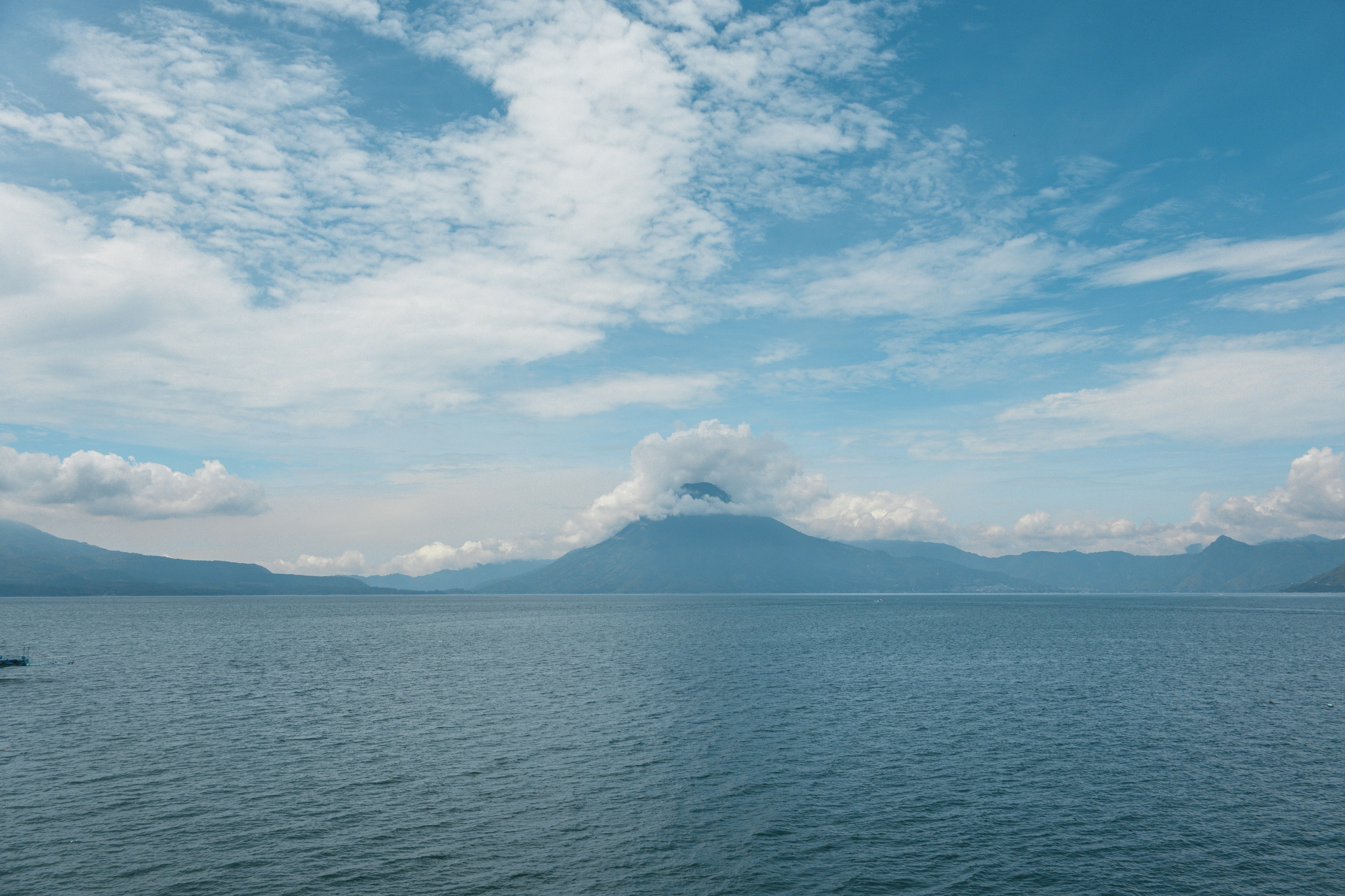 Tranquil boat on expansive lake with a distant mountain and vibrant sky.
