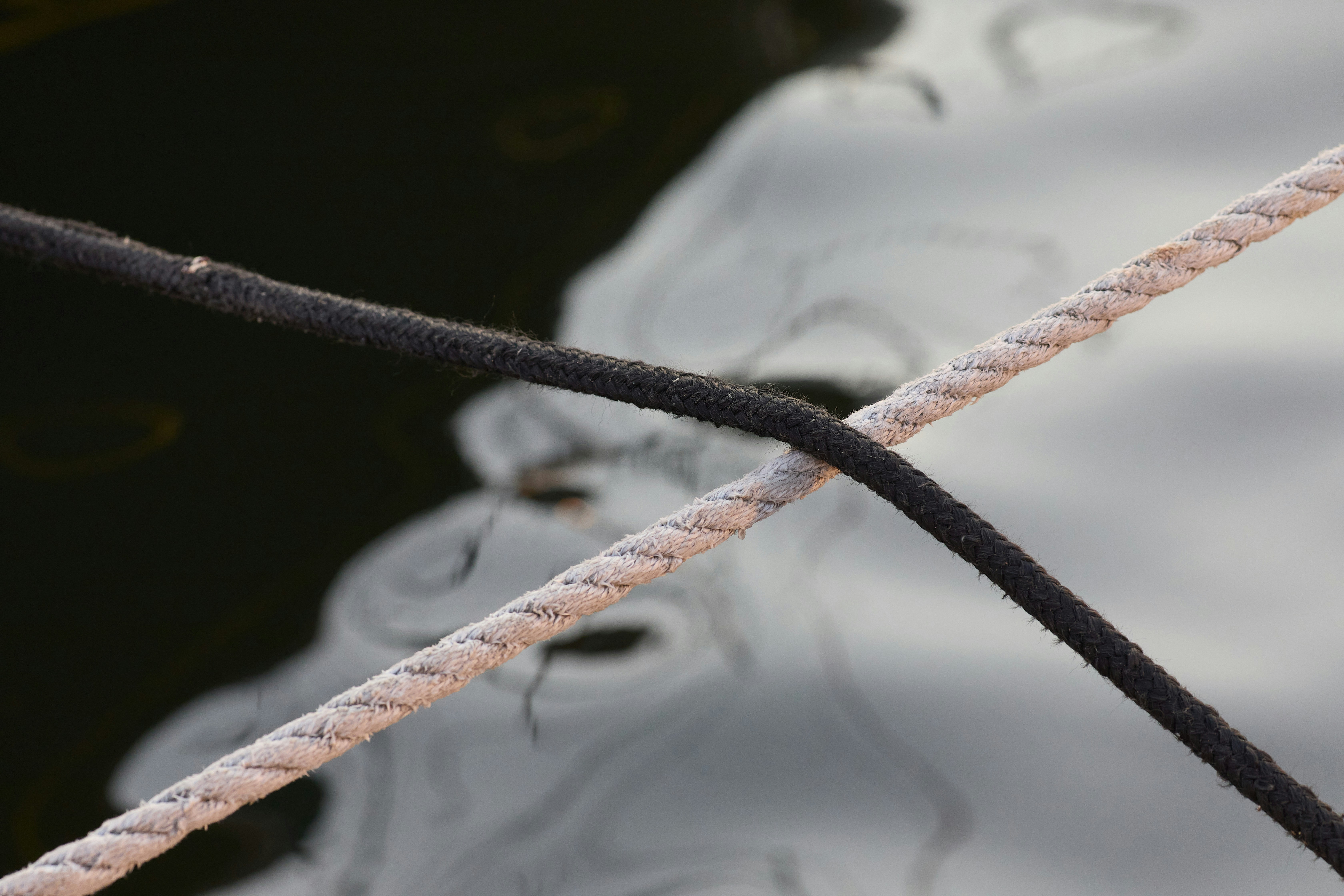 Two ropes intersecting above calm water, creating an abstract interplay of textures and reflections.