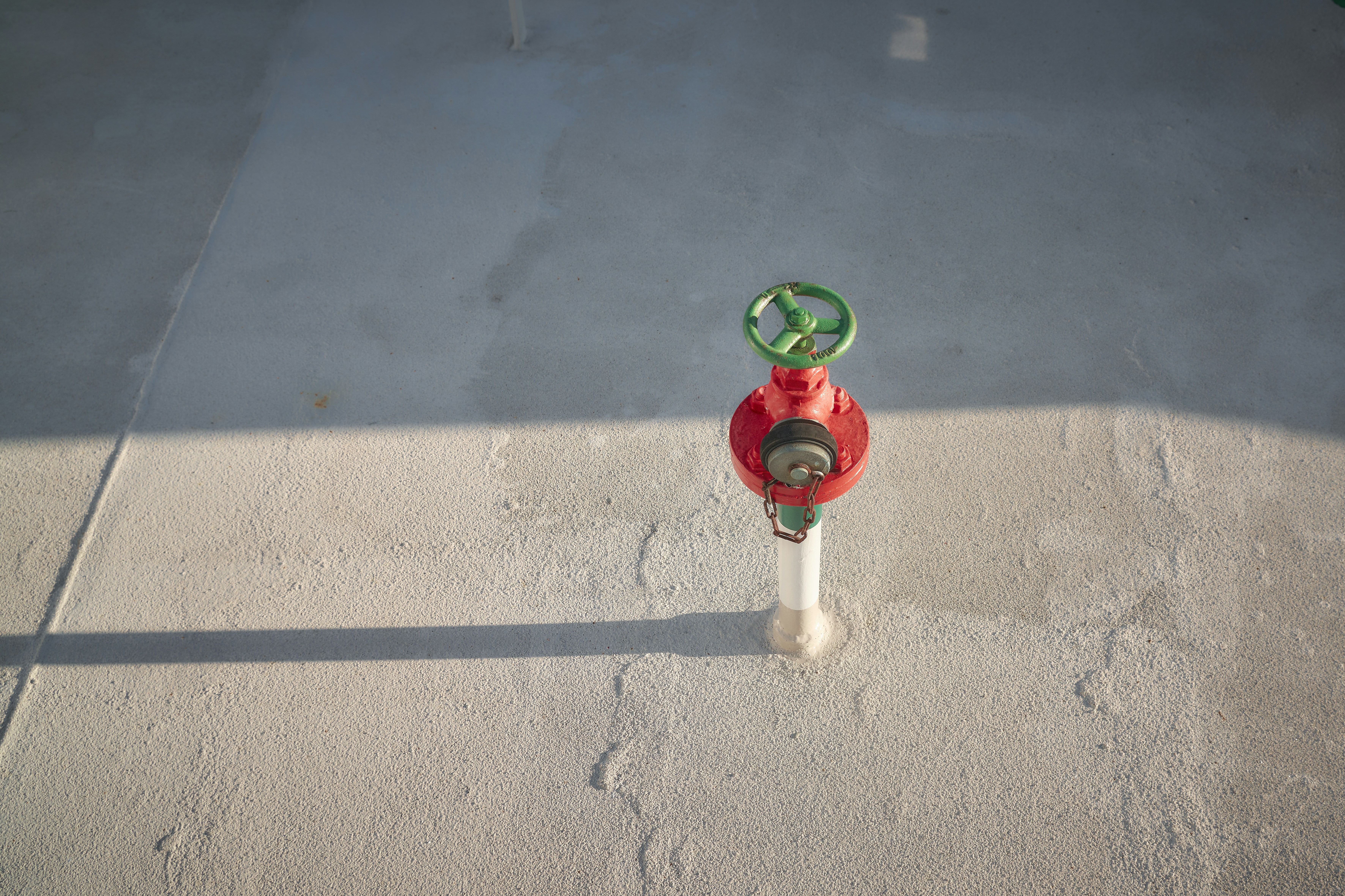Sunlit Red Valve with a Green Handwheel on Concrete