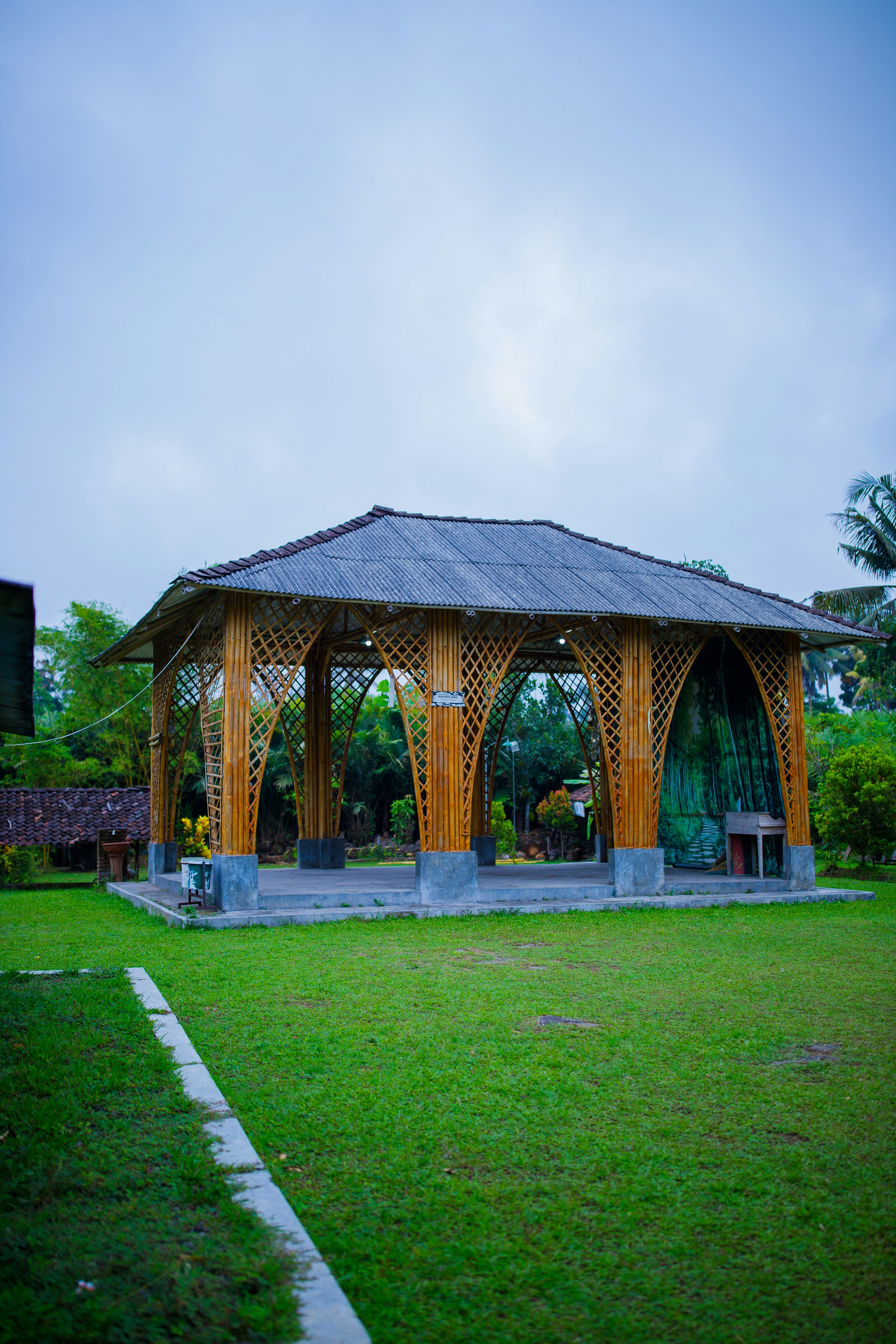 A beautifully crafted bamboo pavilion stands amidst lush greenery, showcasing architectural elegance in a serene outdoor setting.