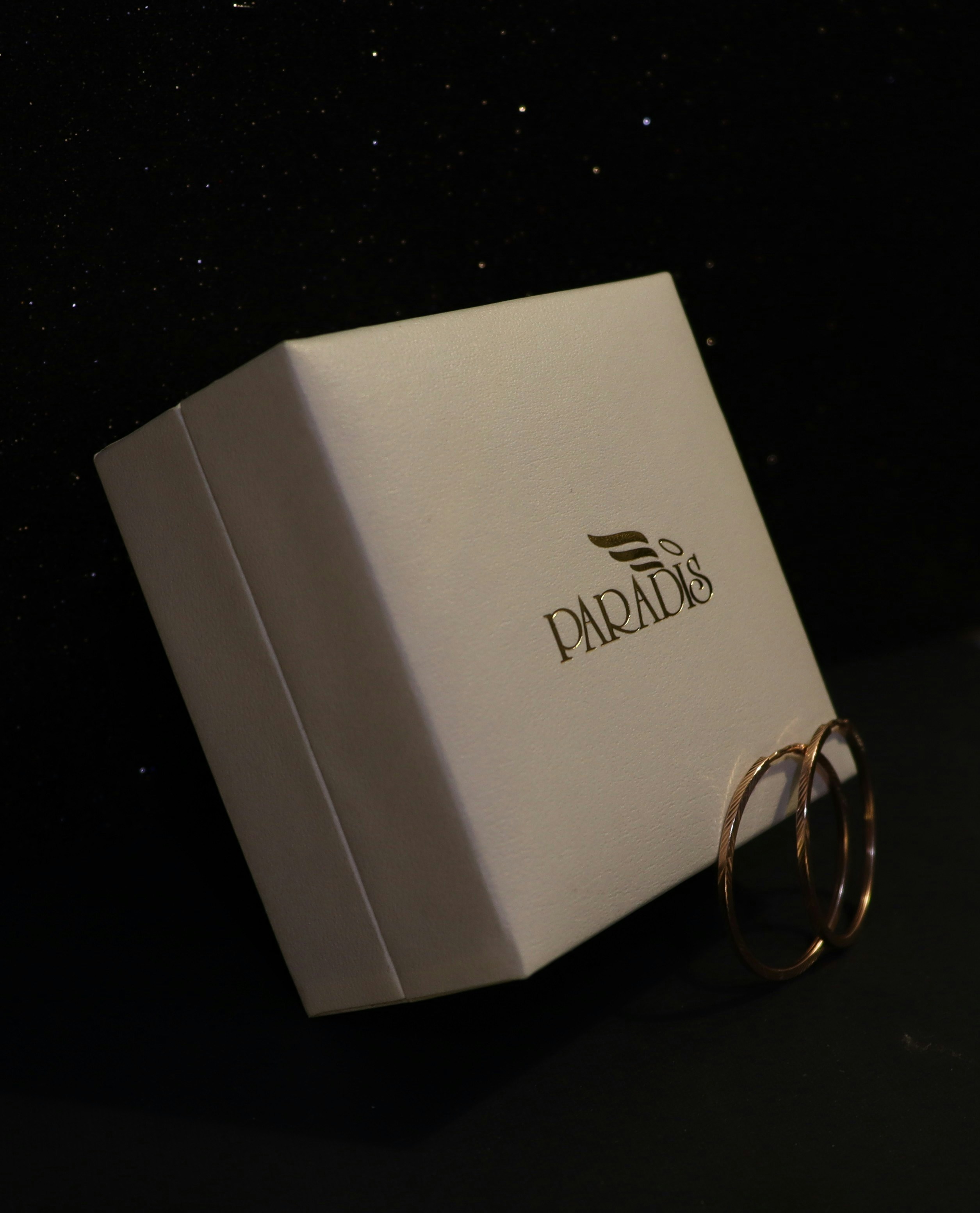 A luxurious jewelry box featuring the brand name 'PARADIS' alongside a pair of elegant hoop earrings, set against a dark, sparkling background.