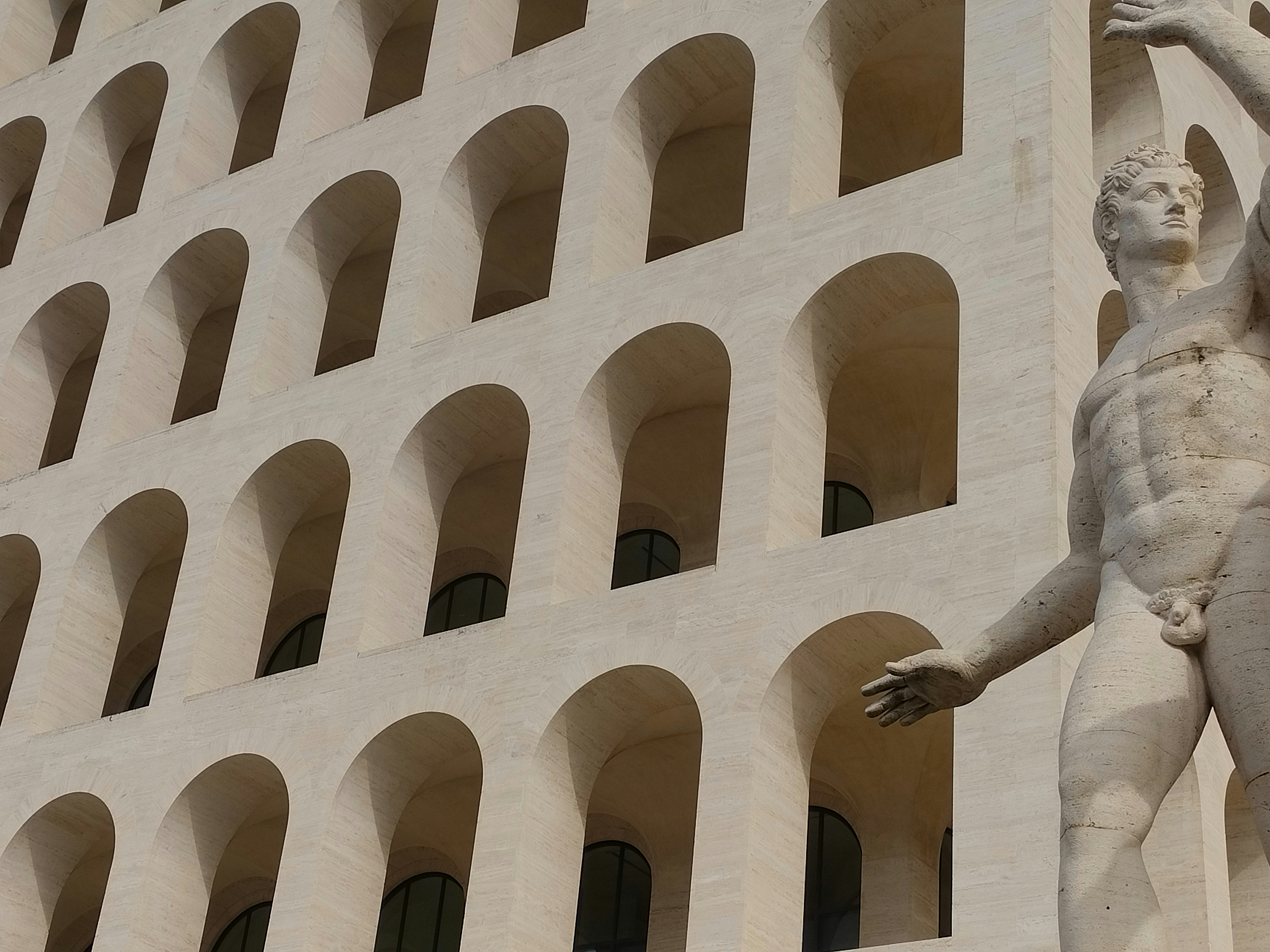 Neoclassical building with repetitive arches and a stone statue in the foreground.