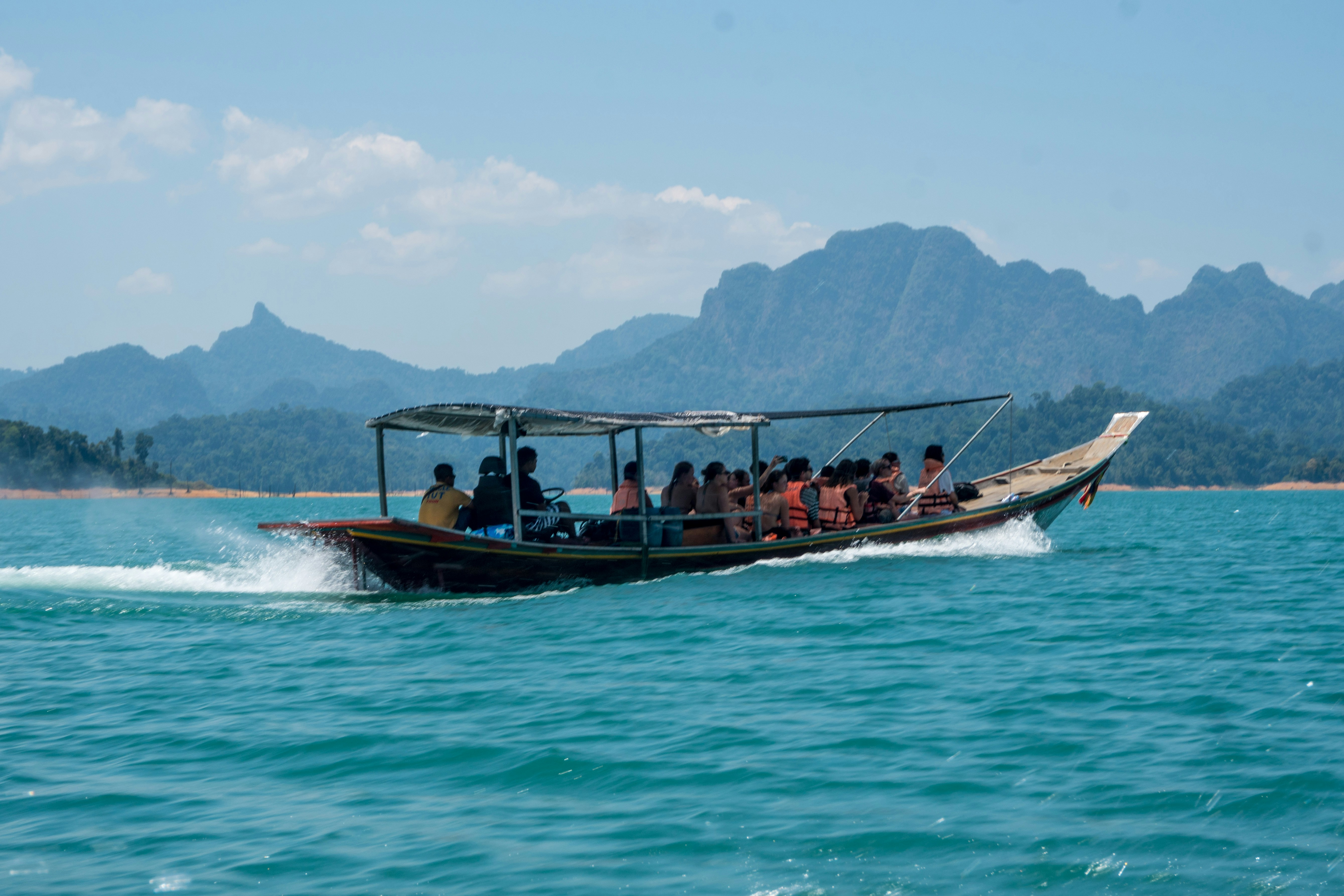 A boat filled with passengers glides through turquoise waters, surrounded by lush mountains under a bright blue sky.