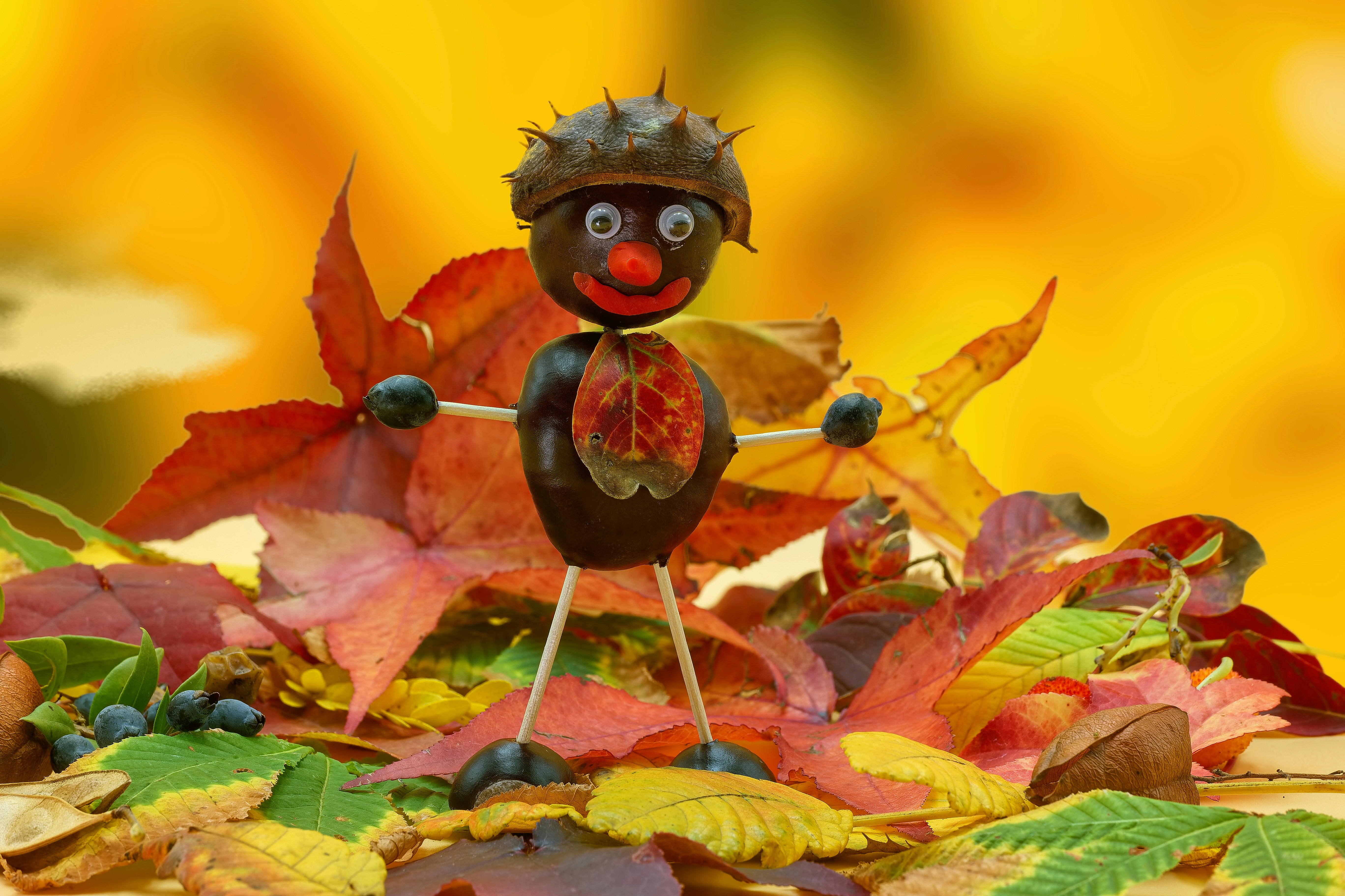 Tiny clay figure with red nose stands amid colorful autumn leaves, creating a whimsical still life. This scene emphasizes a playful character against a vibrant fall backdrop; a small logo-like sculpture sits as the focal point.